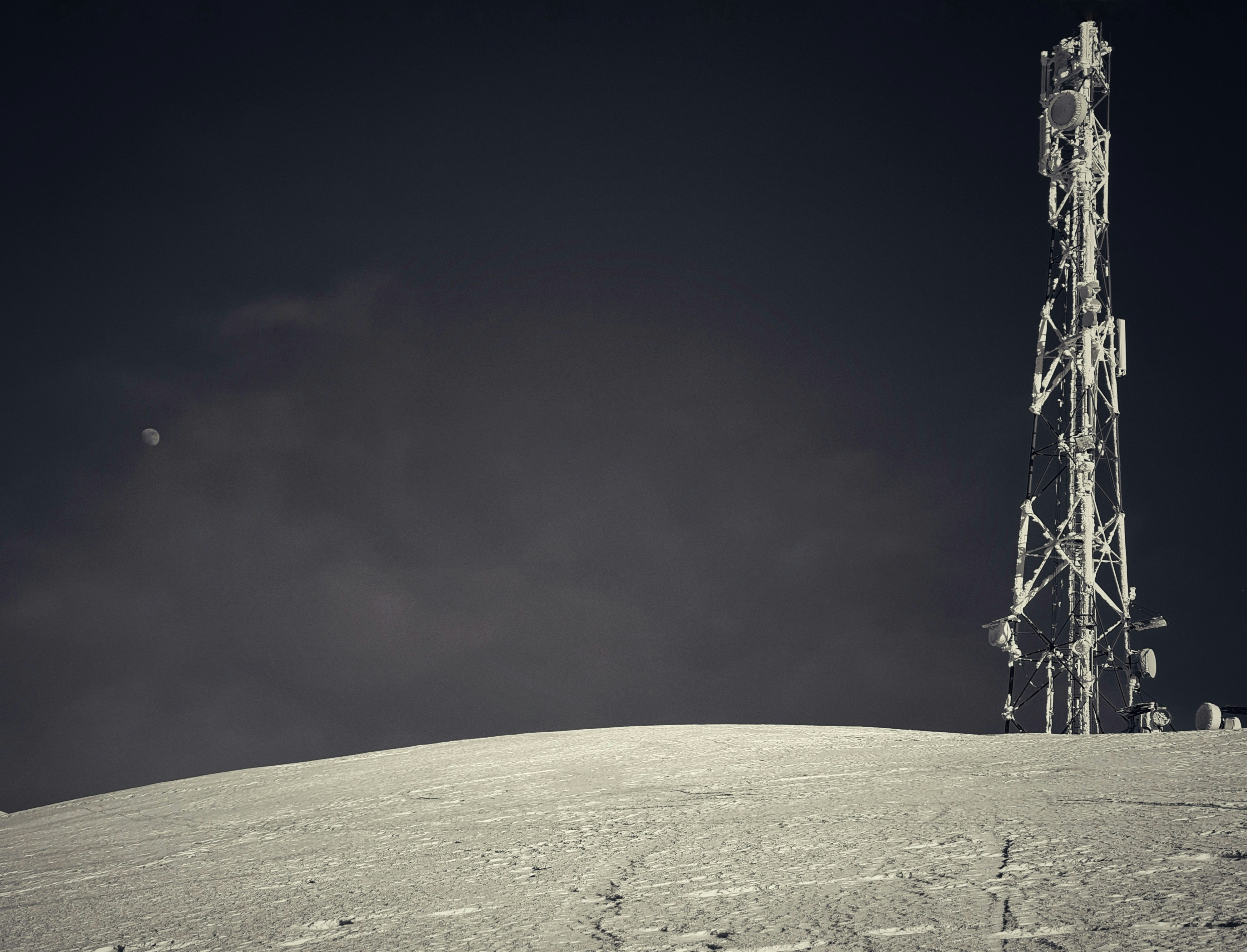 A solitary communication tower stands against a dark sky, surrounded by a vast expanse of snow. The scene captures the stark contrast between technology and nature.