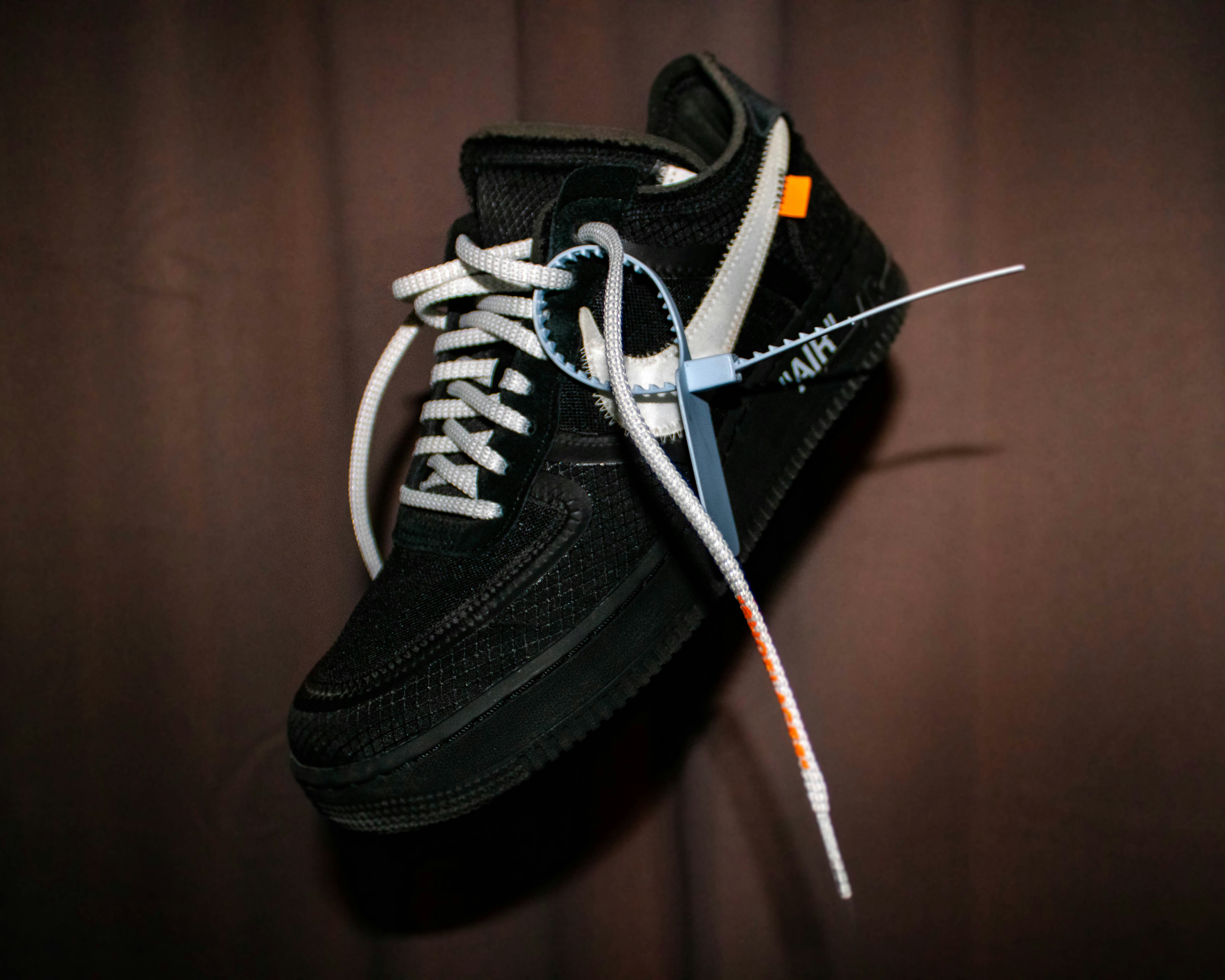 Suspended Sneaker Noir: Black Shoe with Floating Tags on a Dark Wood Floor