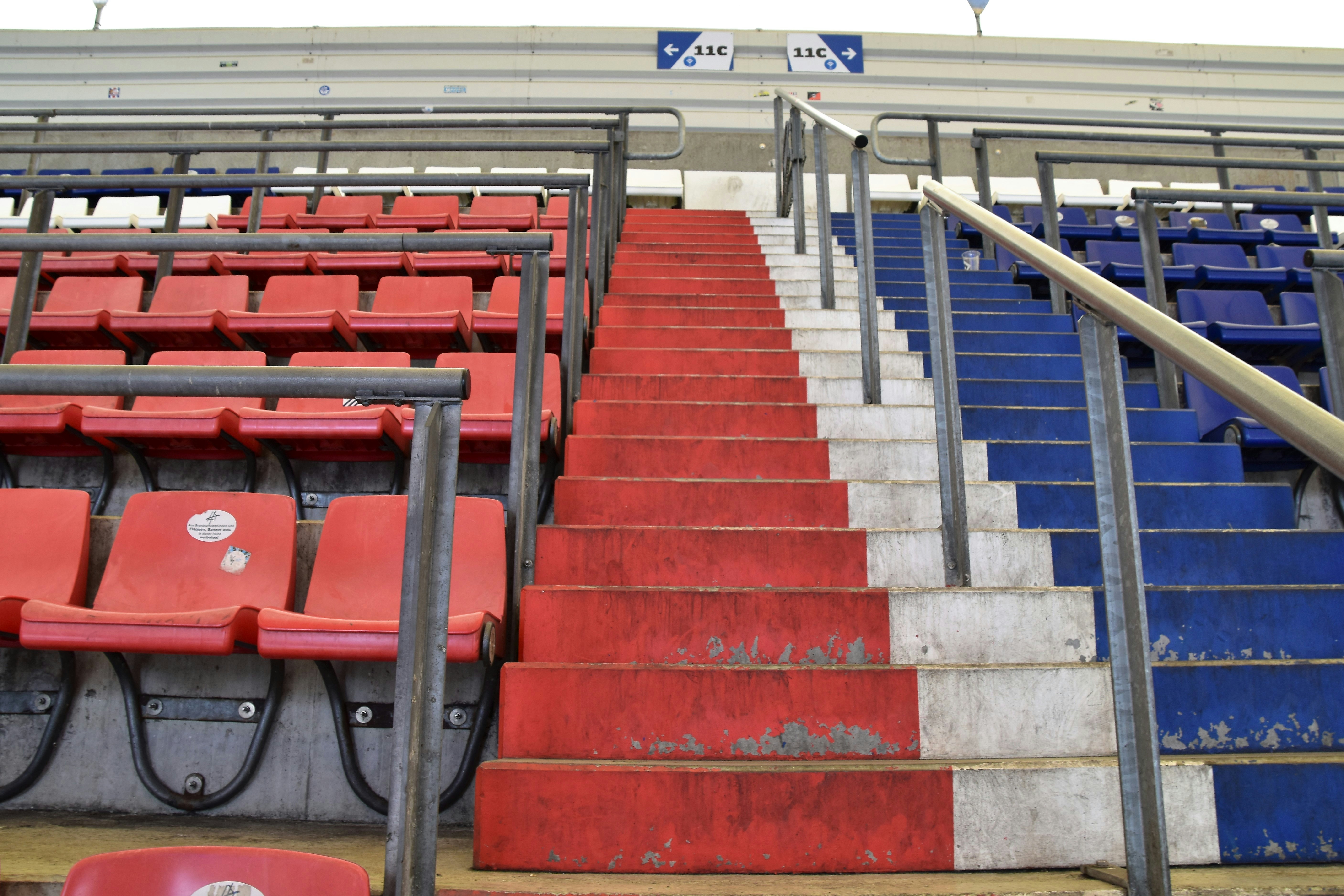 Colorful stadium seating leads up a set of worn steps, showcasing a vibrant mix of red and blue hues. The scene captures the essence of sportsmanship and rivalry.