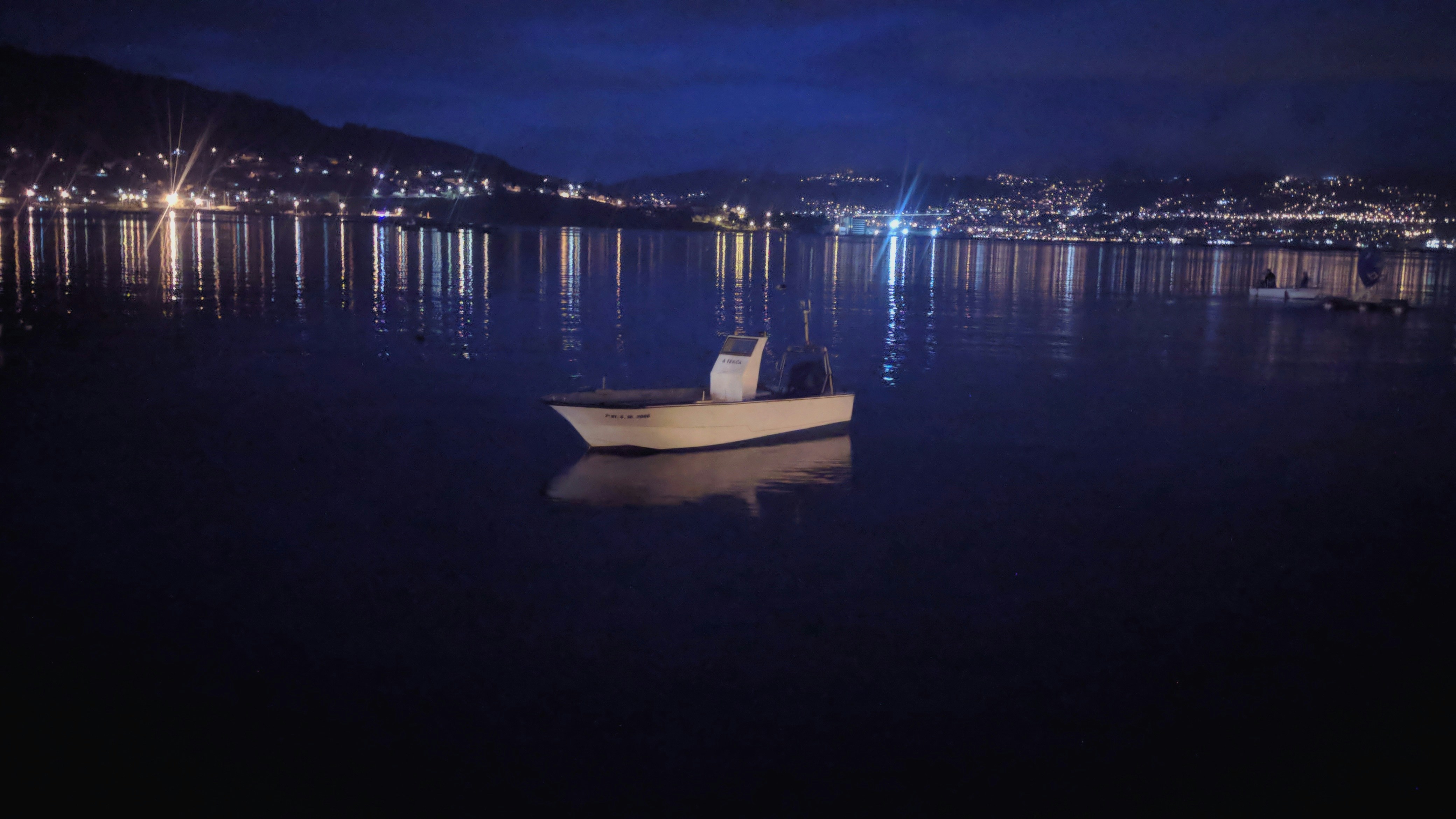 A lone boat floats serenely on calm waters, reflecting city lights against a deep blue twilight backdrop.