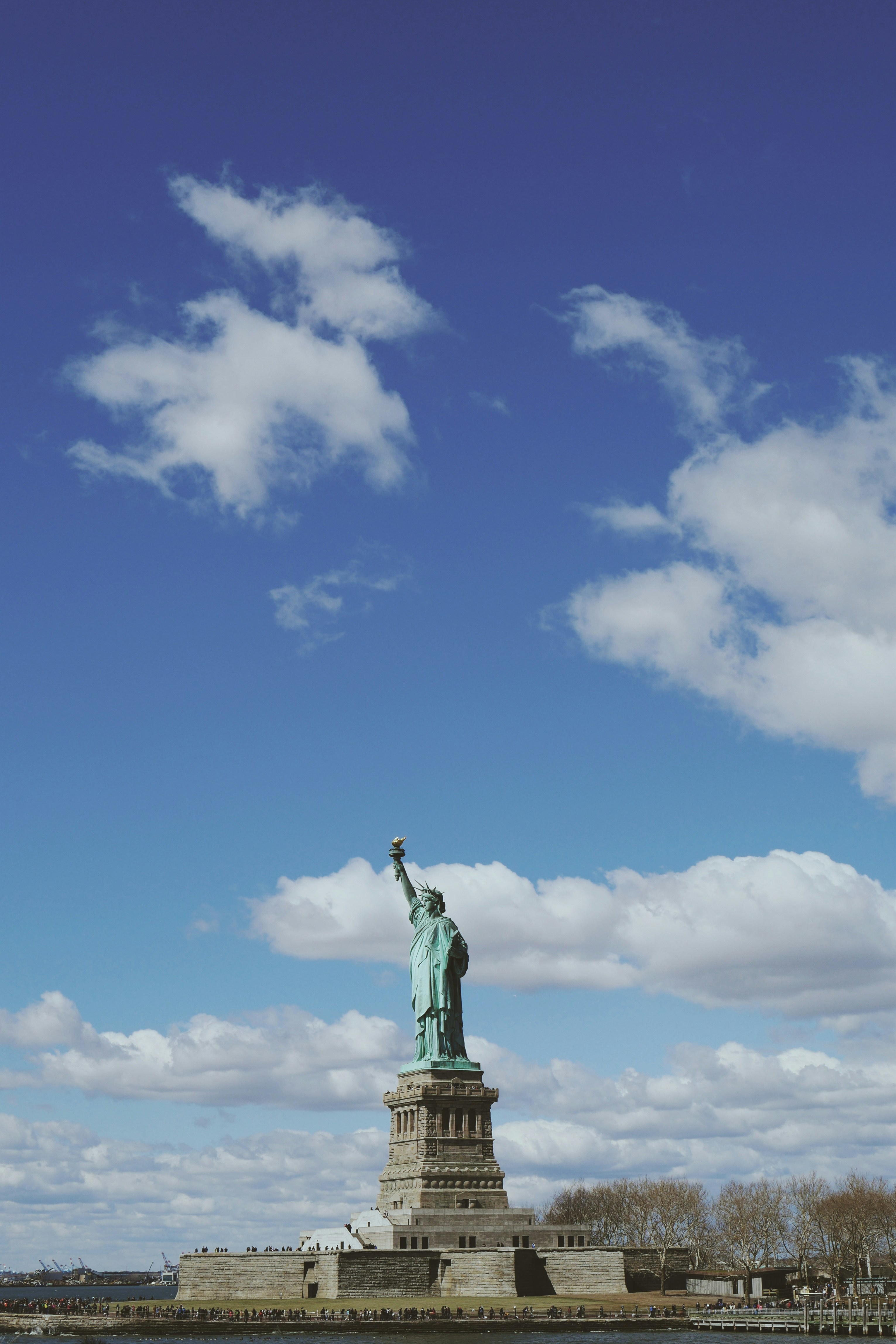 Statue of Liberty standing tall with a vibrant blue sky and scattered clouds in the background.