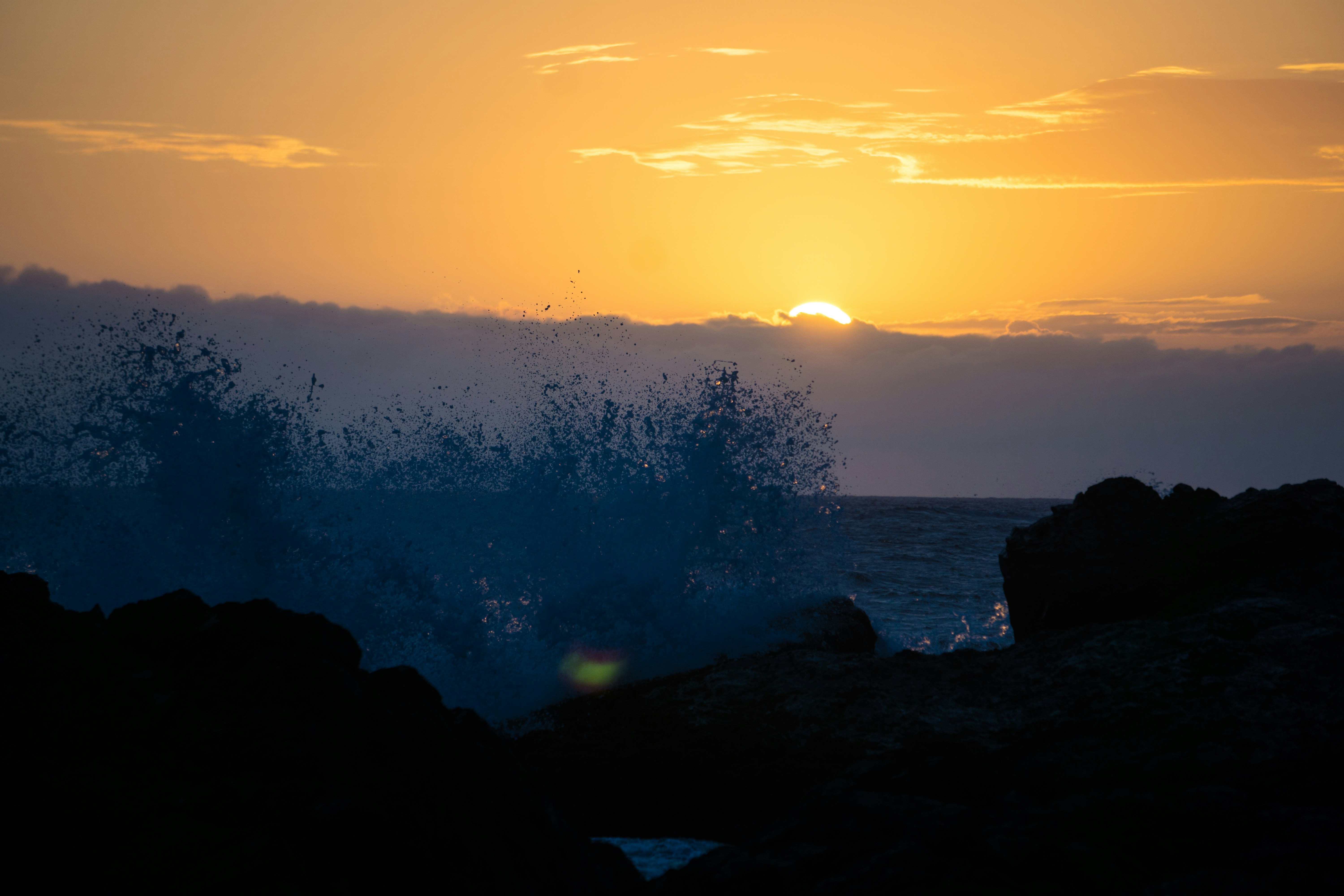 Sunset Clash: Ocean Spray Arcing Over Black Rock Shores