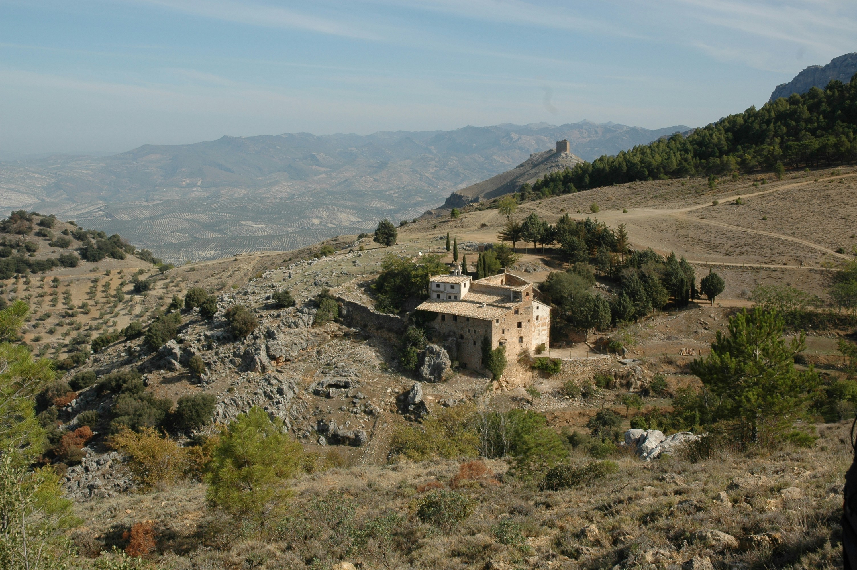 Abandoned stone buildings nestled among rolling hills, with distant mountains stretching under a clear sky.