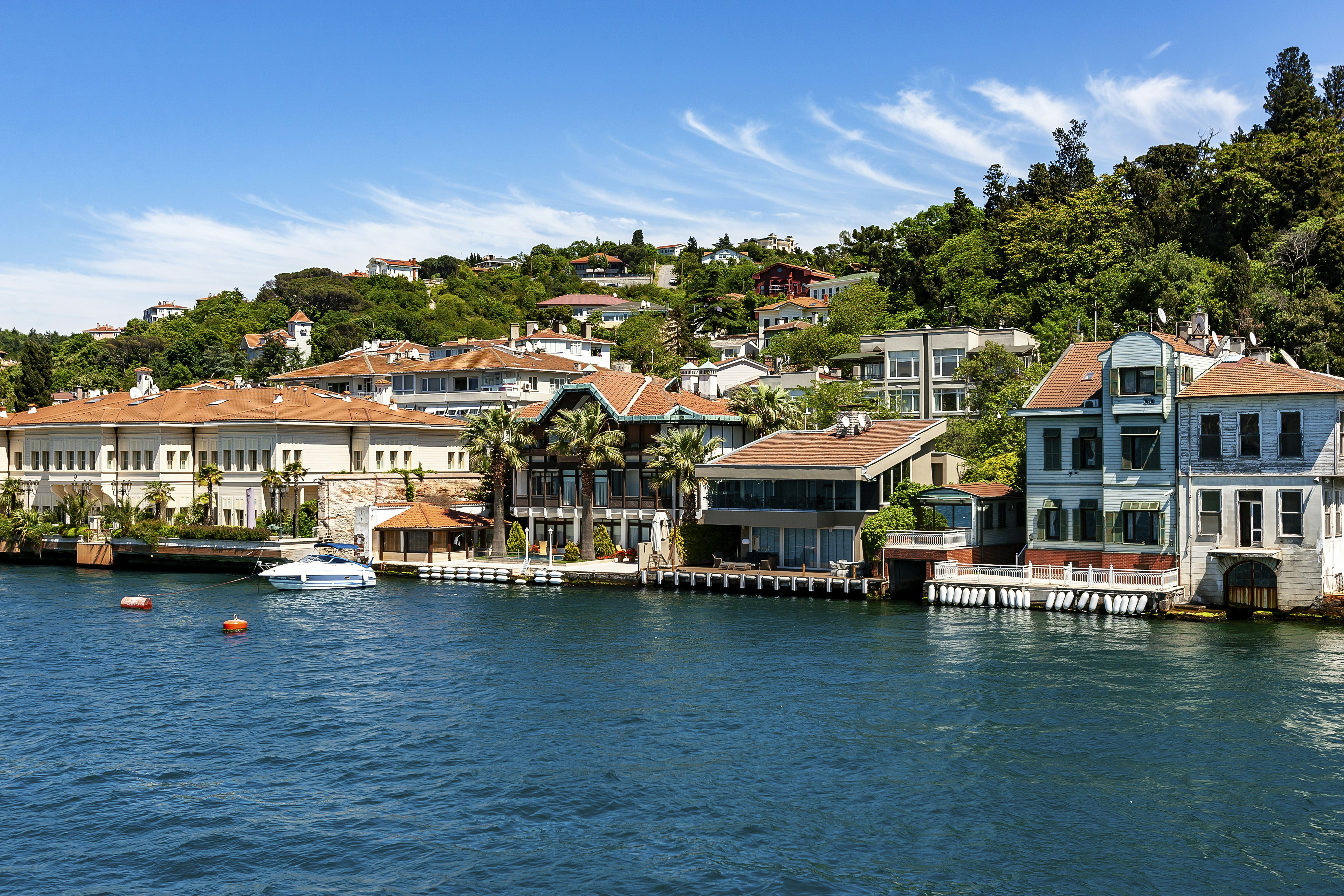Historic buildings line the Bosphorus coast in Istanbul, framed by lush greenery and clear blue skies.