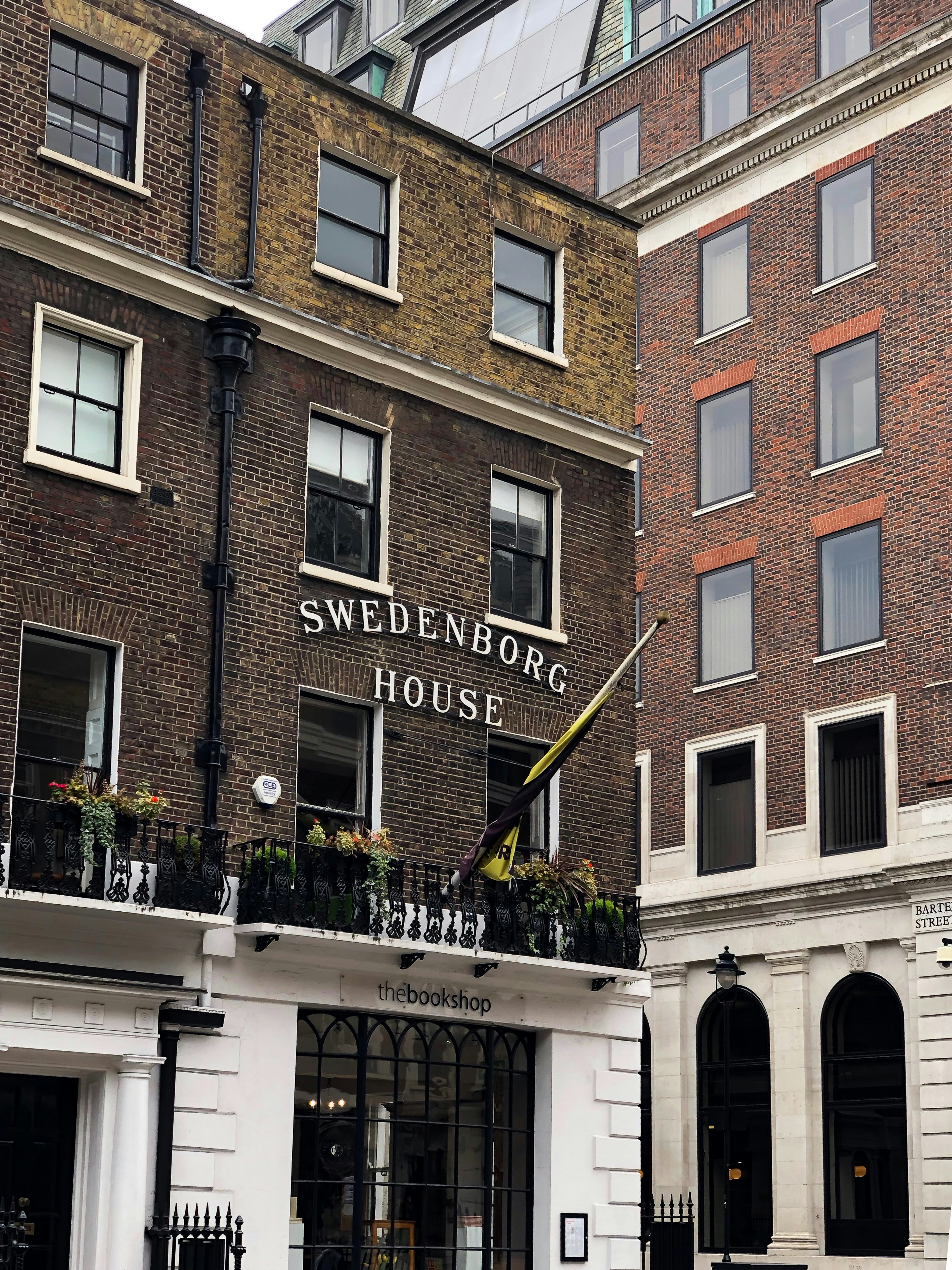 Historic Swedenborg House features elegant architecture with a vibrant bookshop below, surrounded by modern buildings. A flag adds a touch of color to the scene.