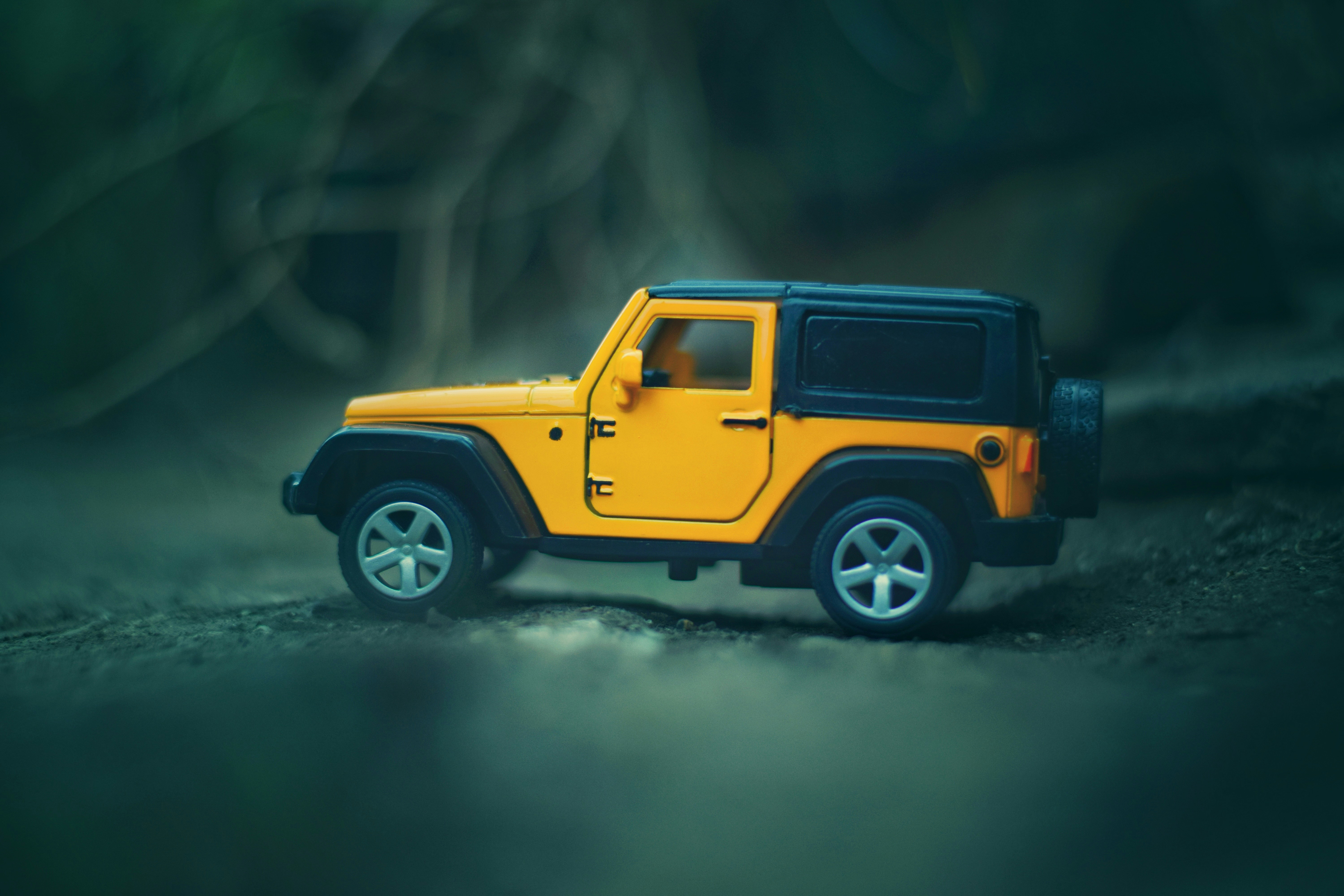A vibrant yellow toy jeep parked on a textured surface, surrounded by blurred green foliage, evoking a sense of exploration.