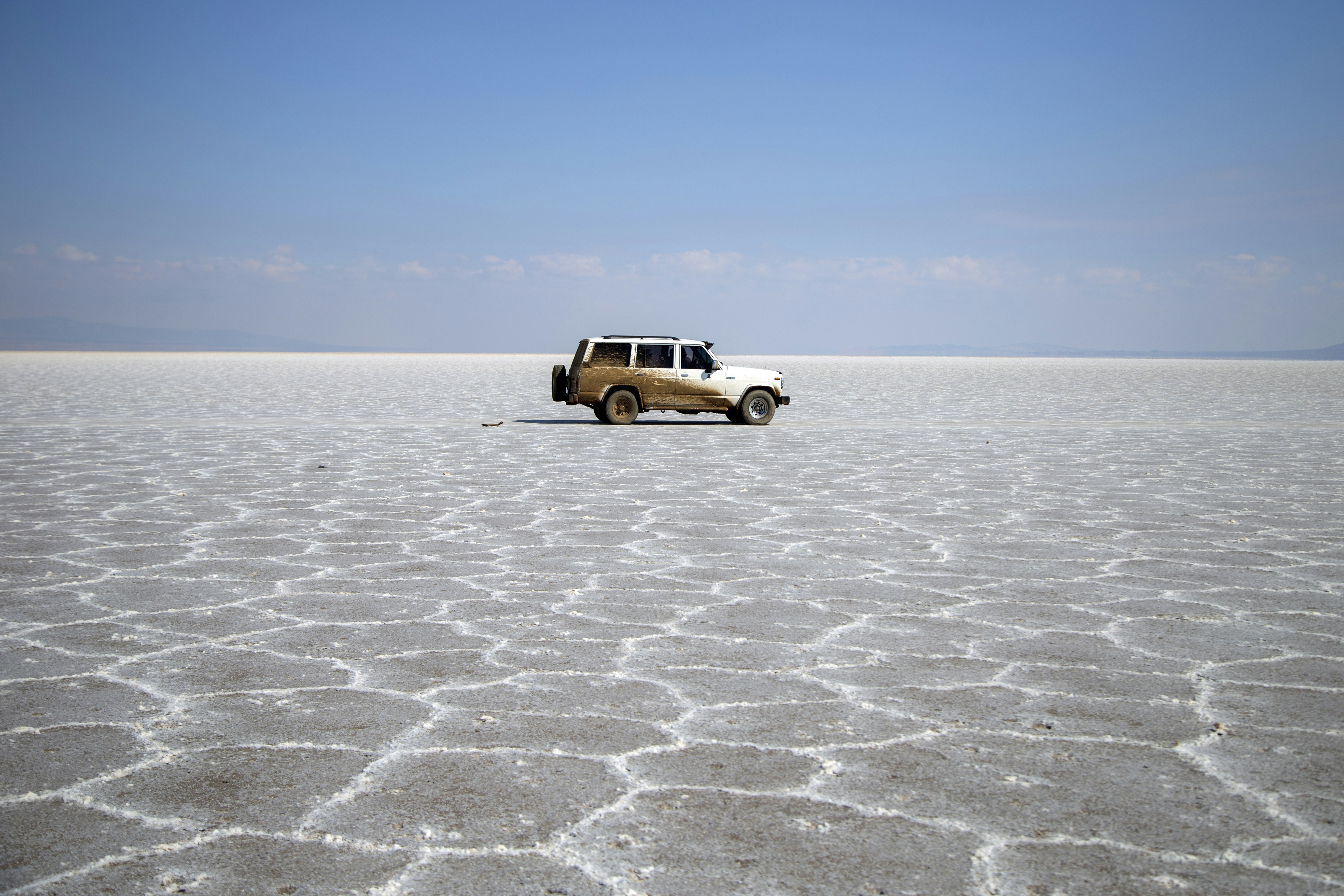 A rugged vehicle navigates the expansive salt flats, showcasing the stark contrast between the vehicle and the arid landscape.