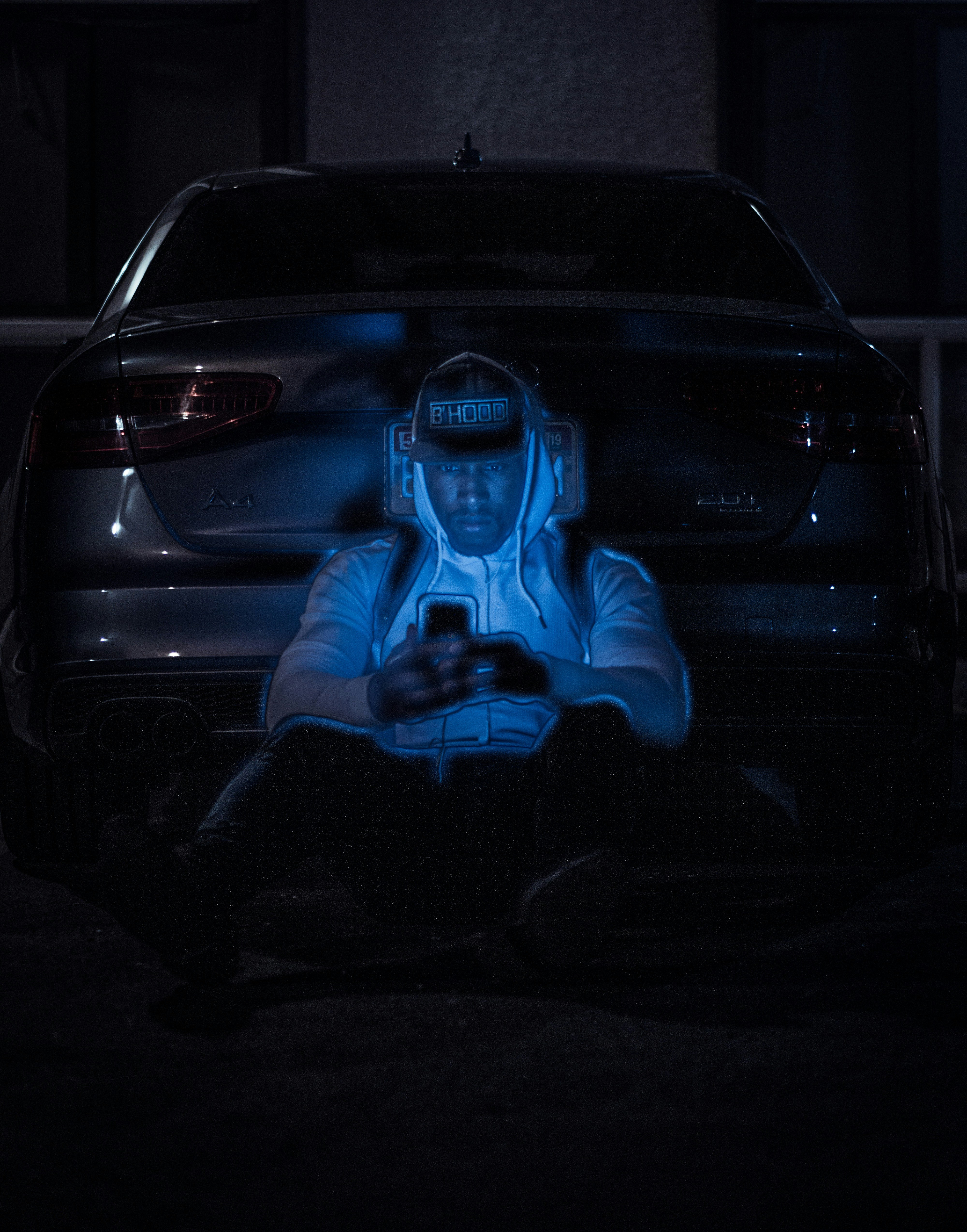 Blue Neon Quietude: Hoodie and Phone Glow Before a Parked Car