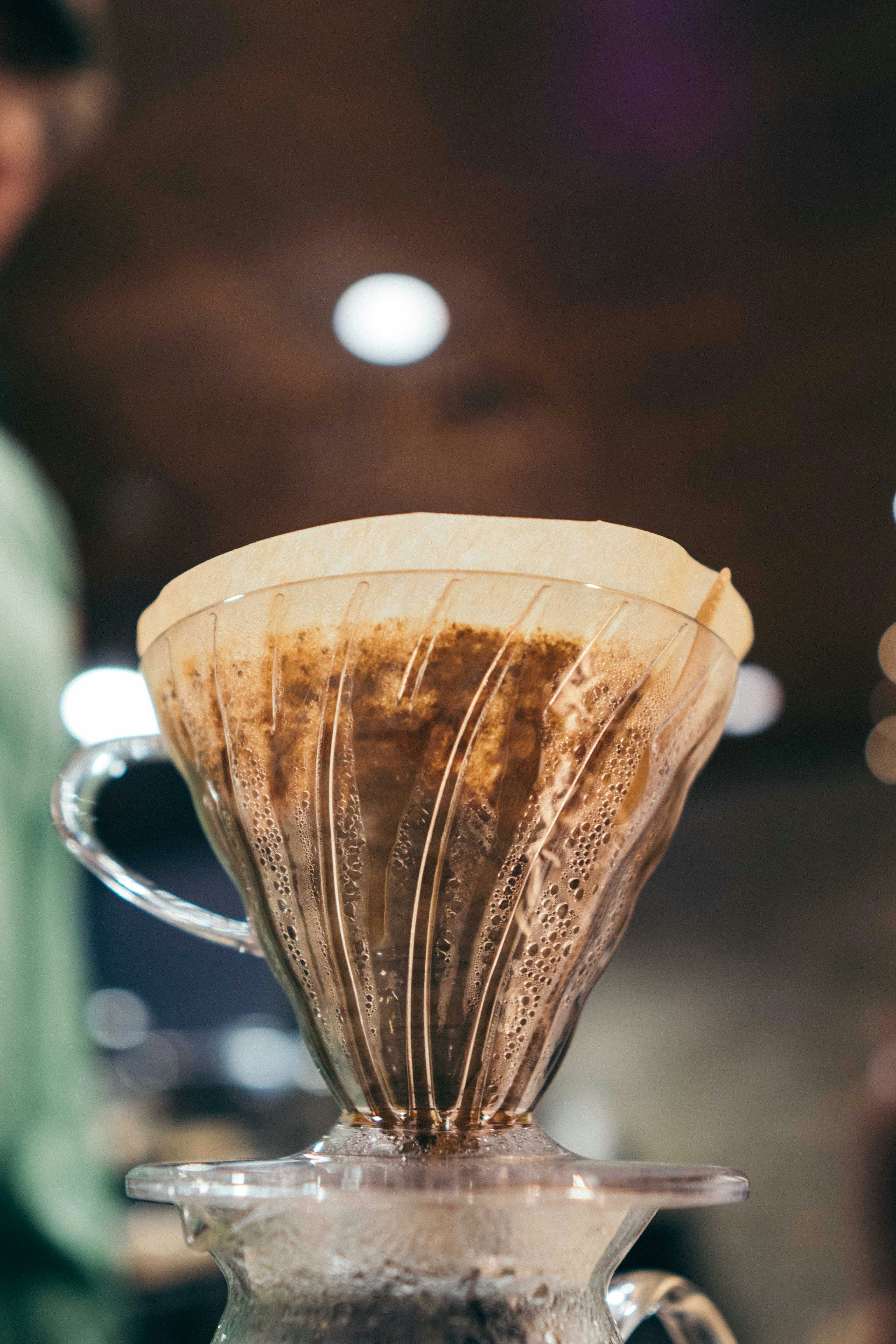 Coffee filter filled with grounds, brewing aromatic coffee through a glass dripper. Steam rises, enhancing the sensory experience.