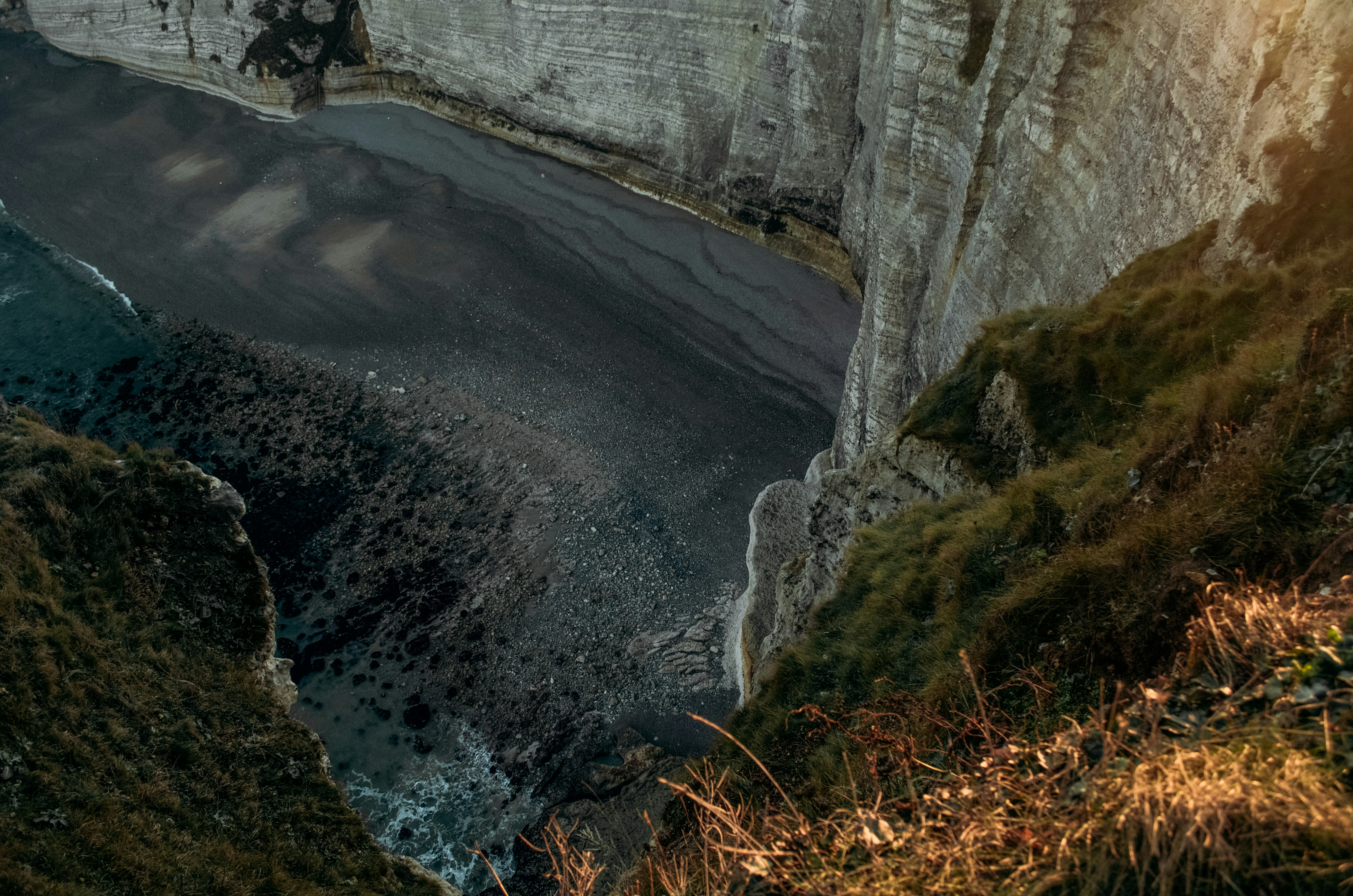 Aerial view of a rugged coastline with steep cliffs meeting a tranquil beach, showcasing the interplay of rock and sand. The scene captures the serene yet dramatic essence of nature's landscape.