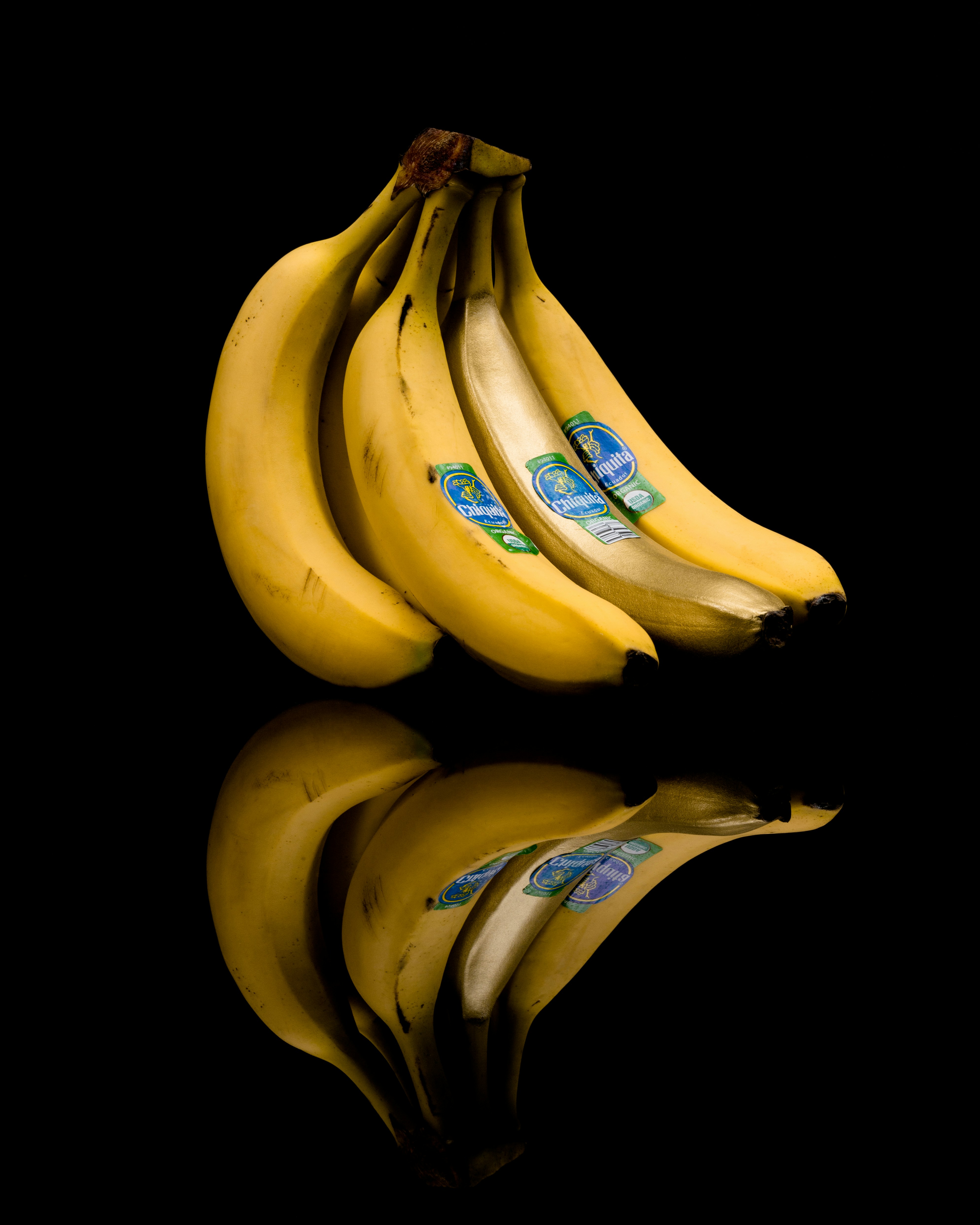 A cluster of ripe bananas with distinctive labels, beautifully reflected on a black surface.