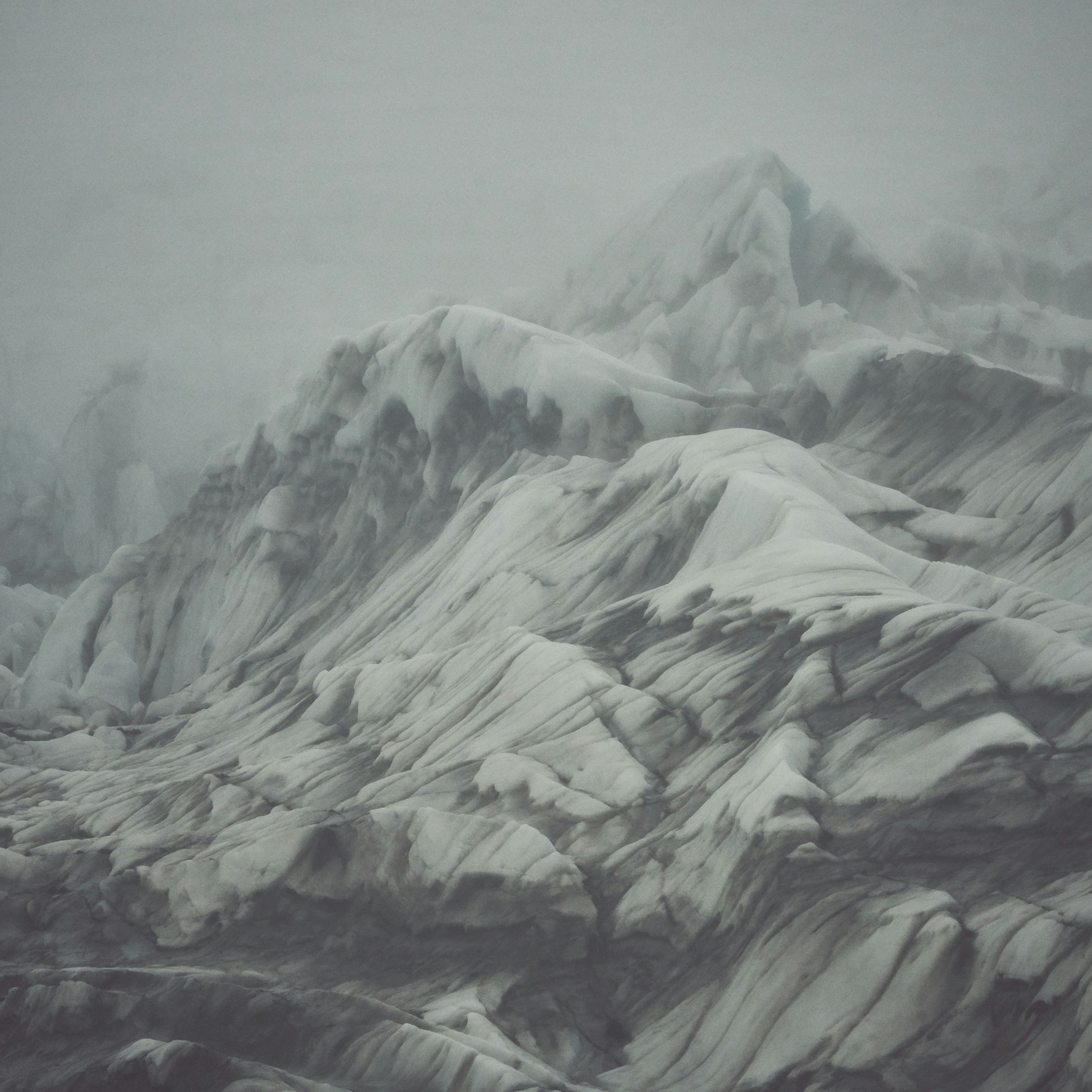 Textured ice formations and rugged peaks merge in a moody, mist-laden scene, evoking the raw beauty of glacial environments.