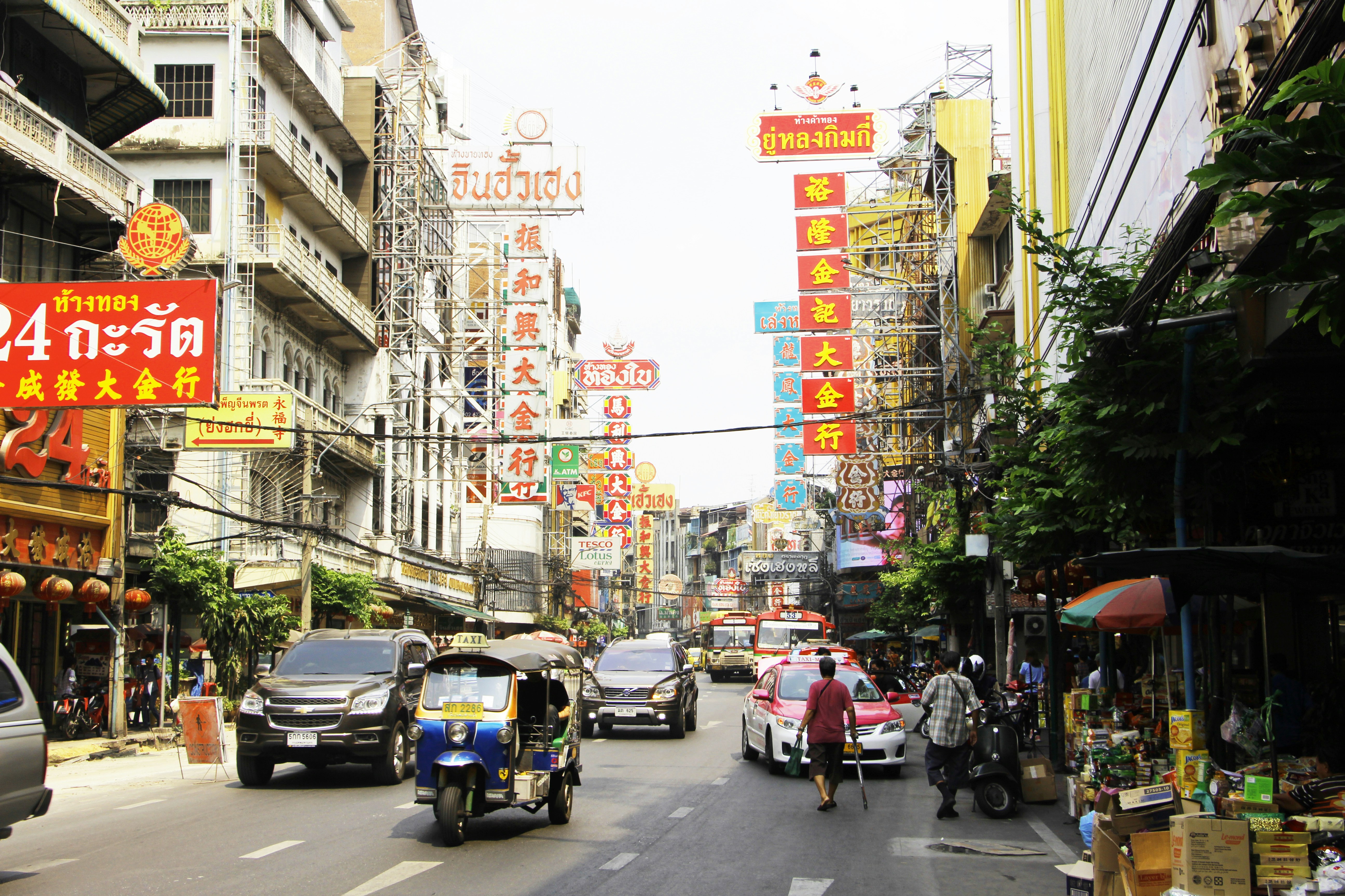 Busy street scene in Chinatown with colorful signs, bustling traffic, and vibrant storefronts under a bright sky.