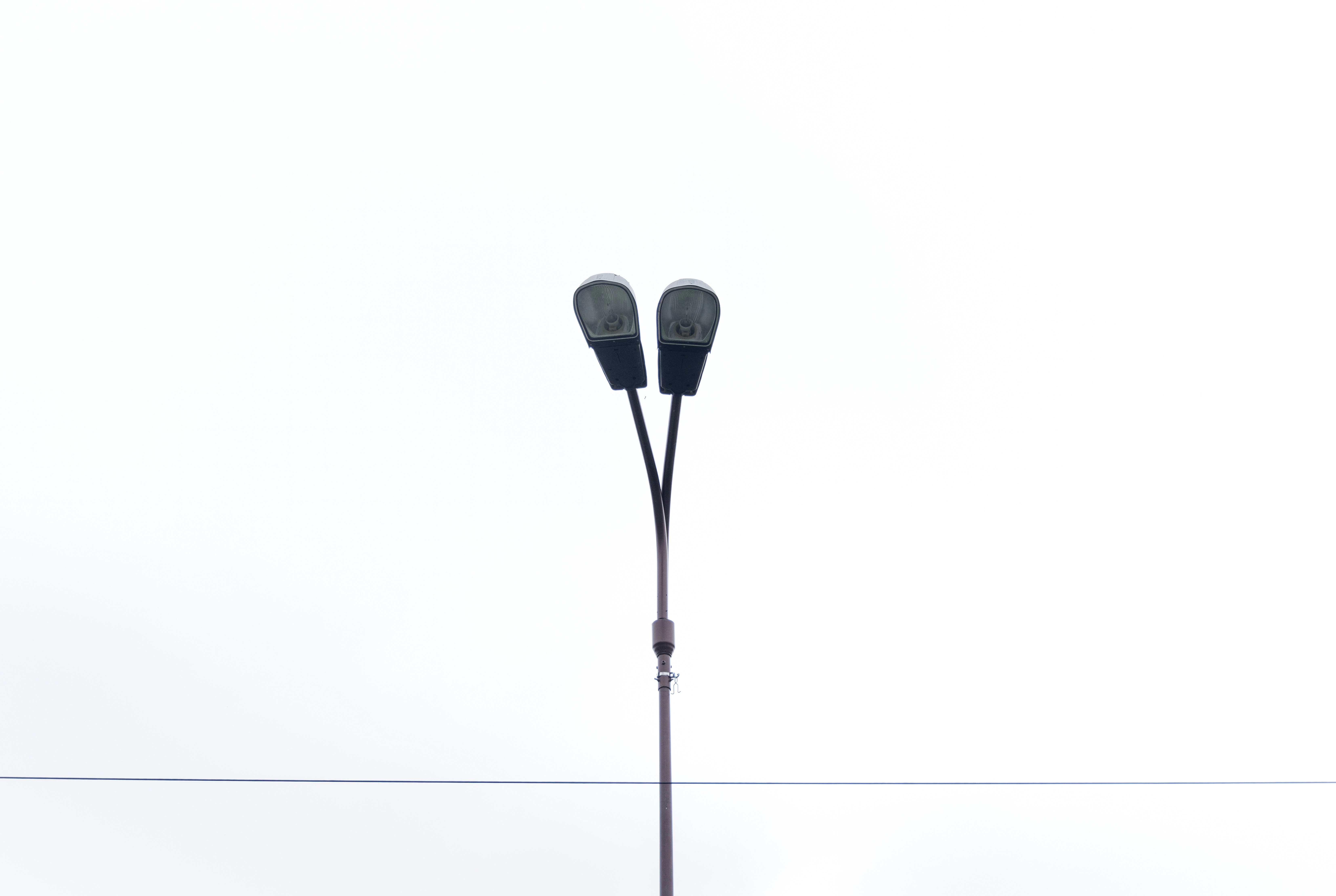 Two streetlights mounted on a single pole against a bright, overcast sky.