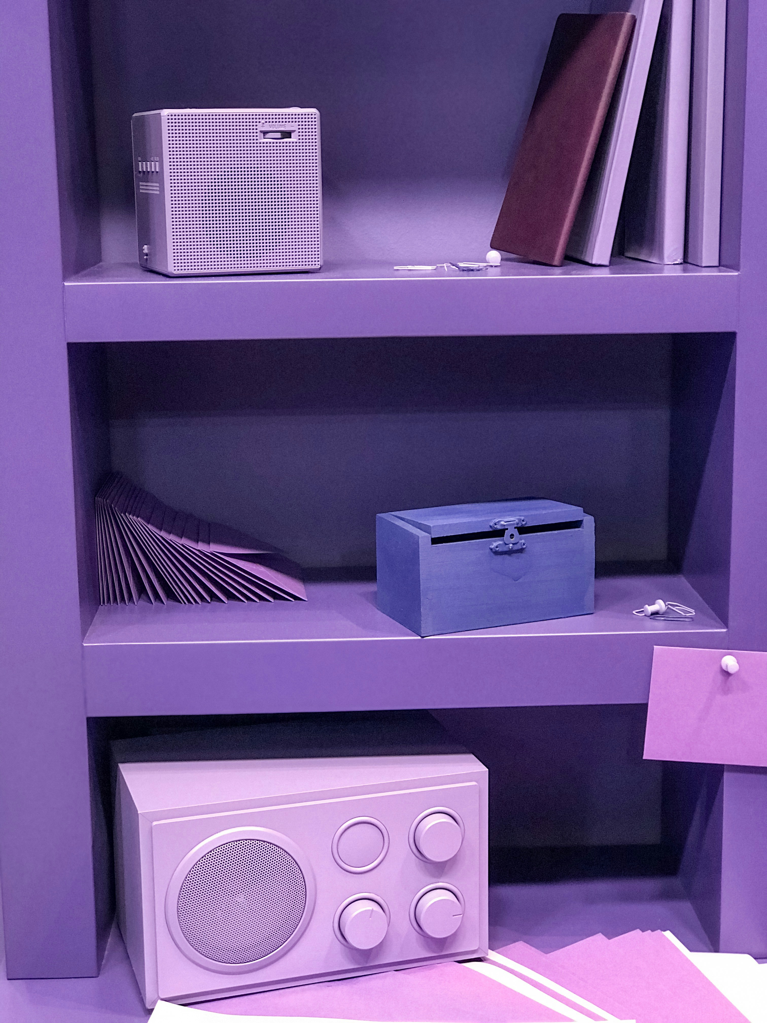 A vibrant purple bookshelf displaying a blend of objects including a speaker, notebooks, and a decorative box, creating a playful yet organized aesthetic.