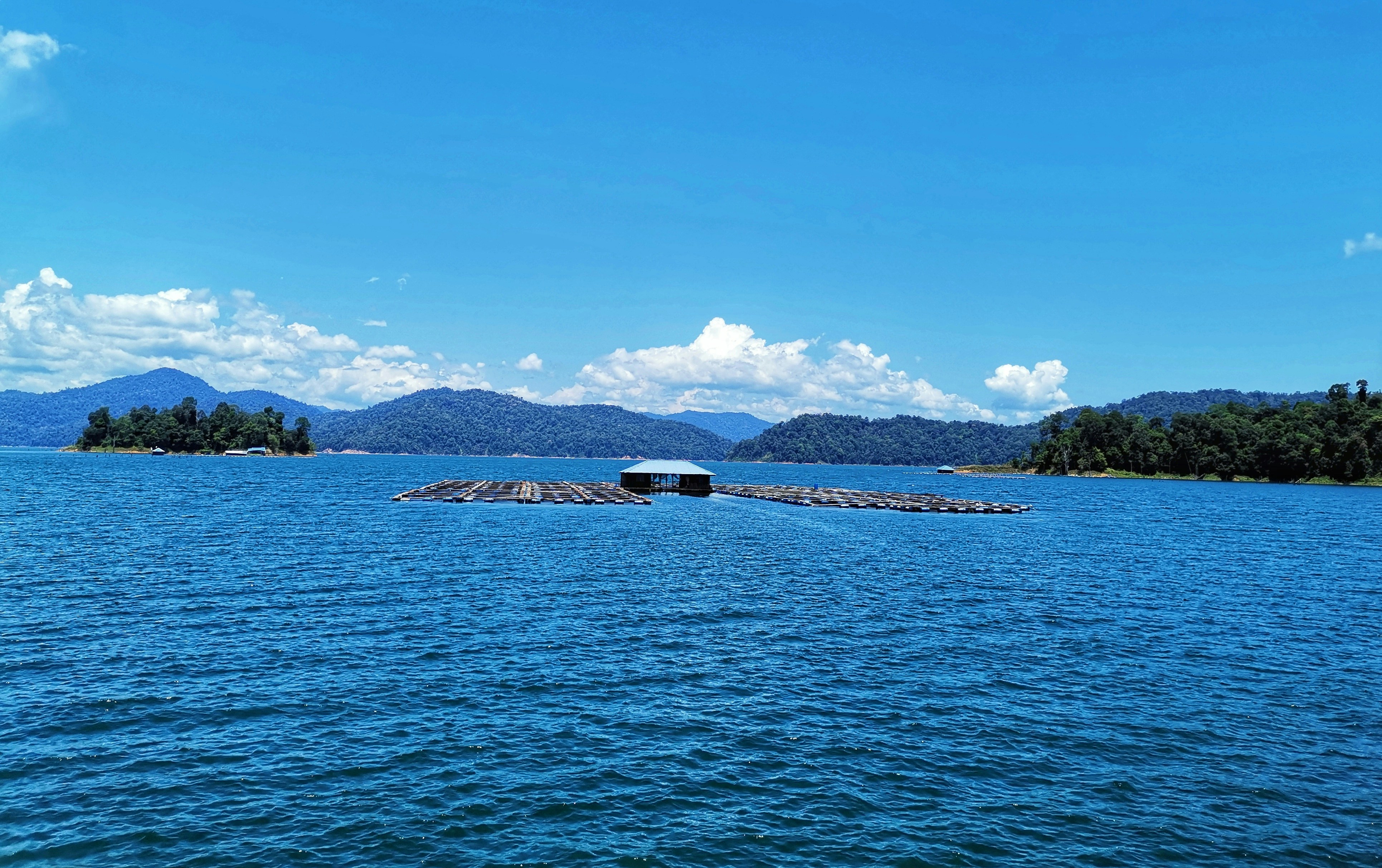 Calm blue waters with small islands under a clear sky, surrounded by distant mountains.