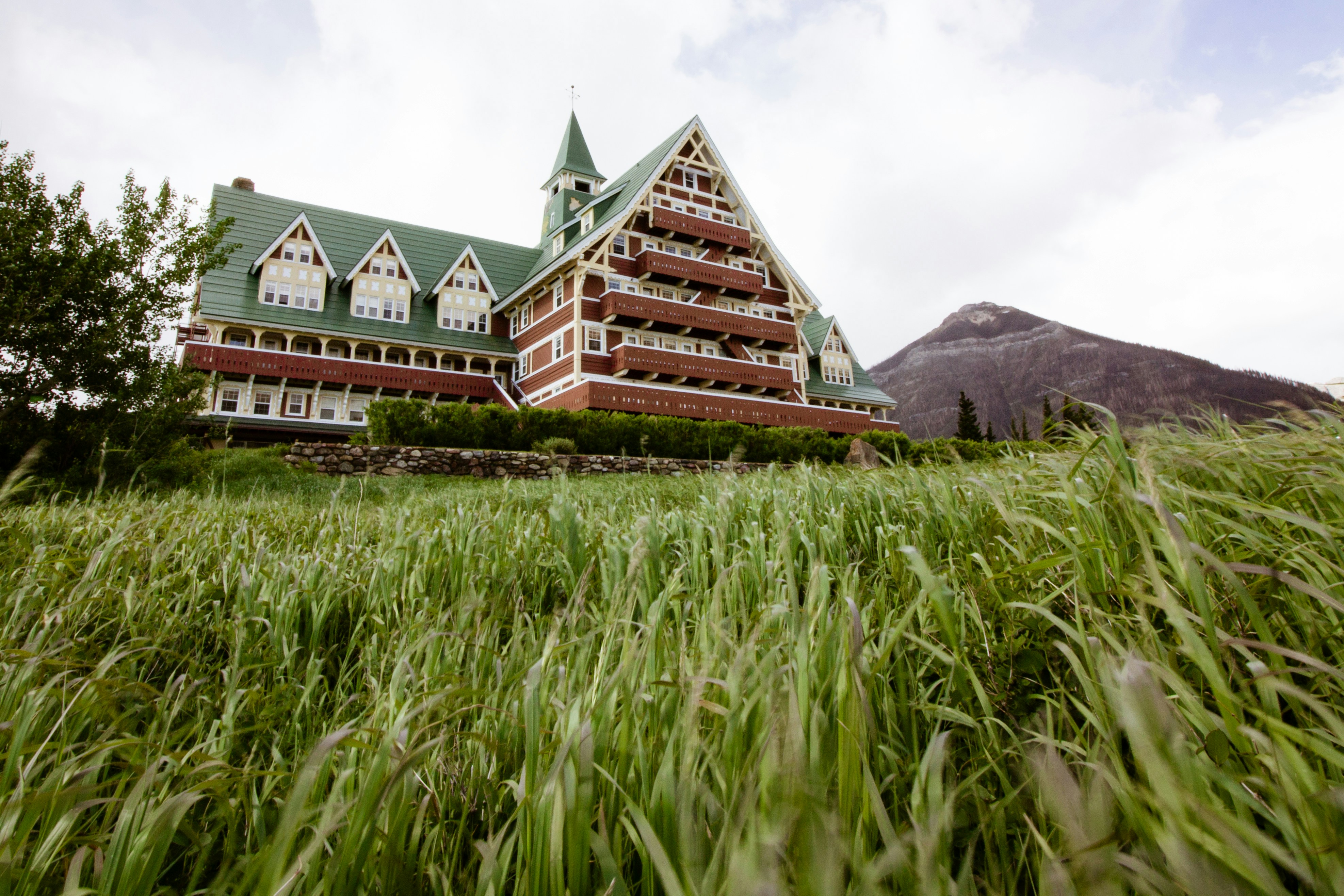 Historic lodge nestled among lush green grass with a mountainous backdrop. Architectural details reflect a blend of traditional and alpine styles.