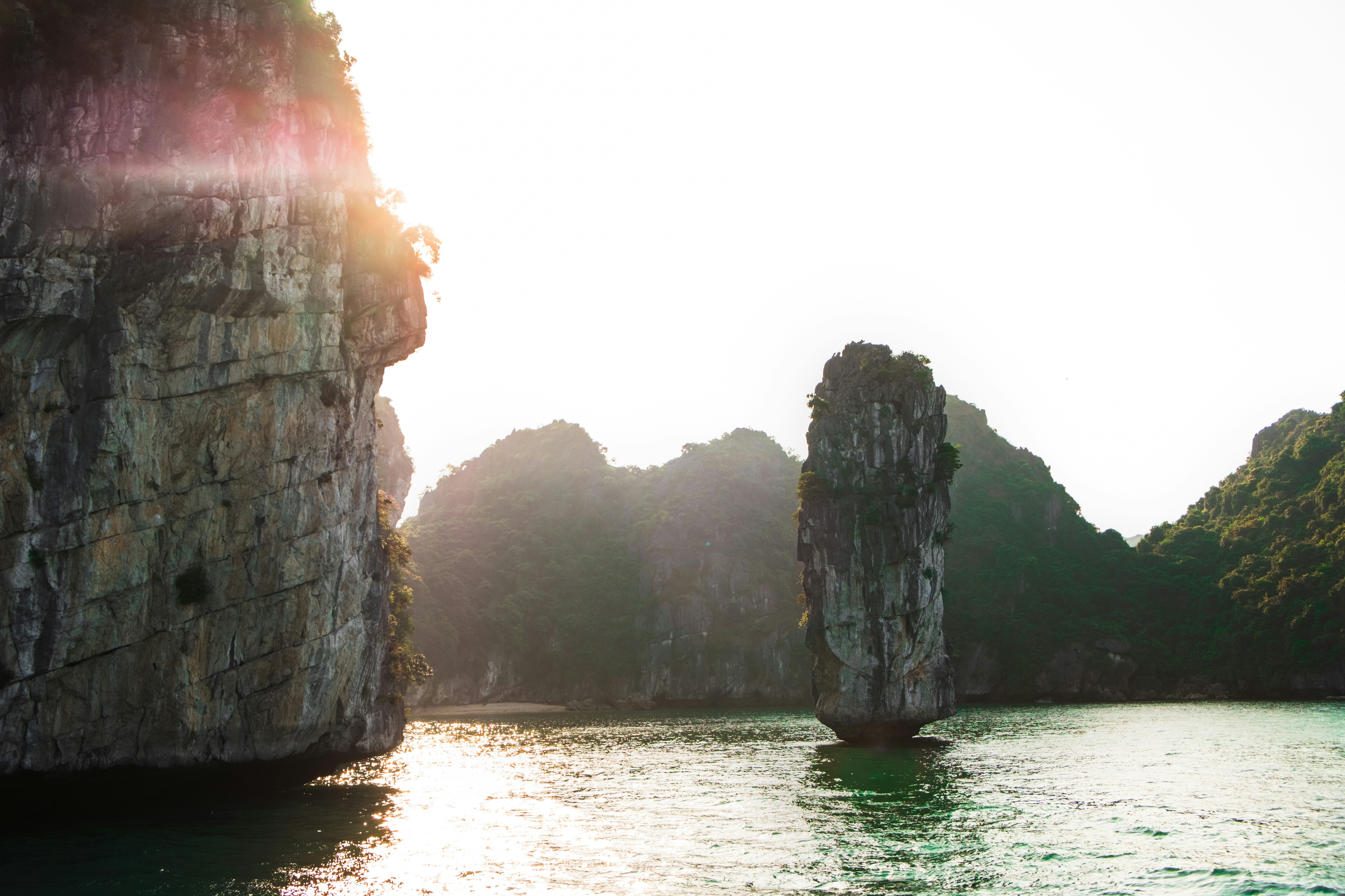 Dramatic limestone formations rise from tranquil waters, illuminated by soft sunlight in a serene landscape.