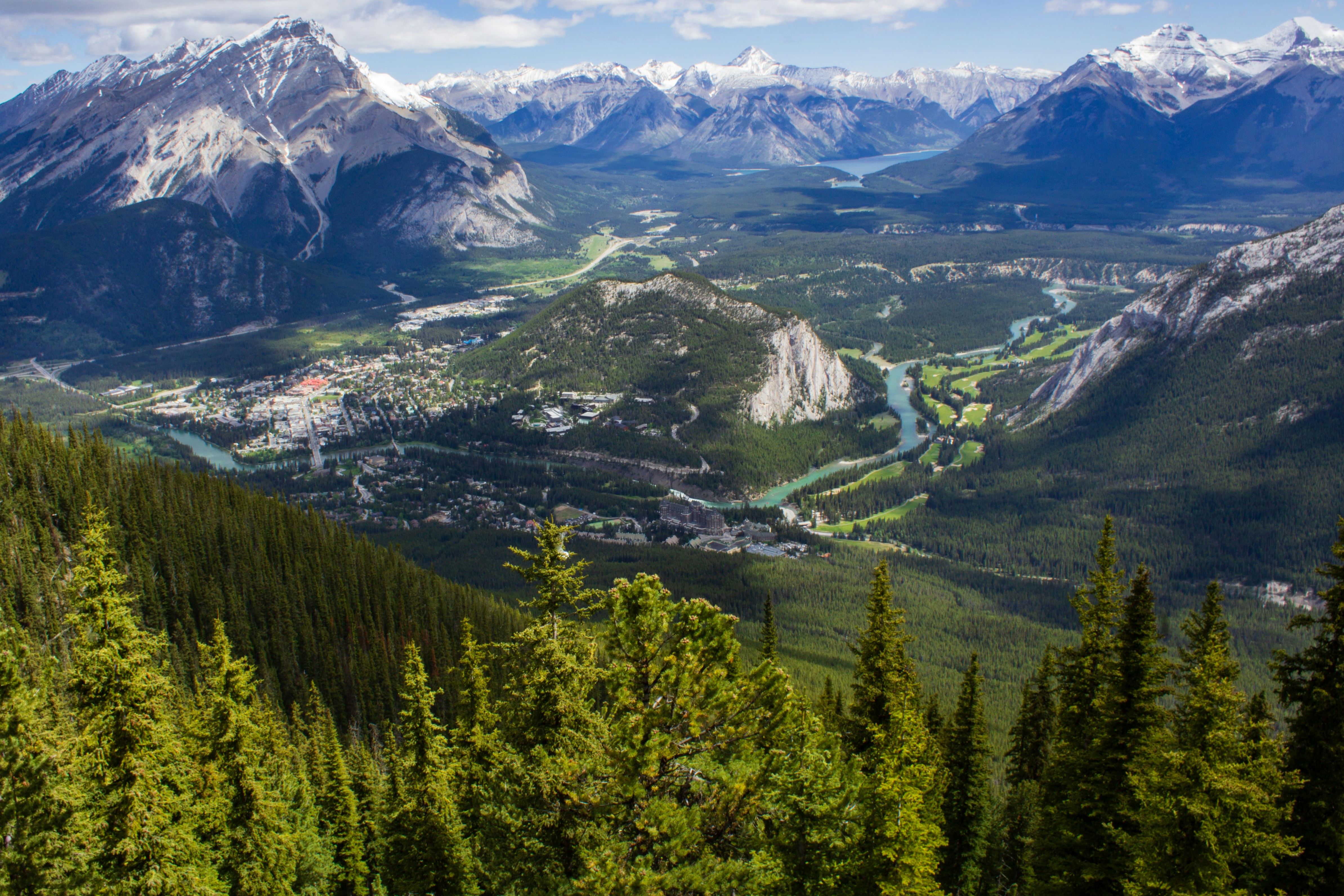 Panoramic view of Banff nestled among lush forests and towering mountains under a bright sky.