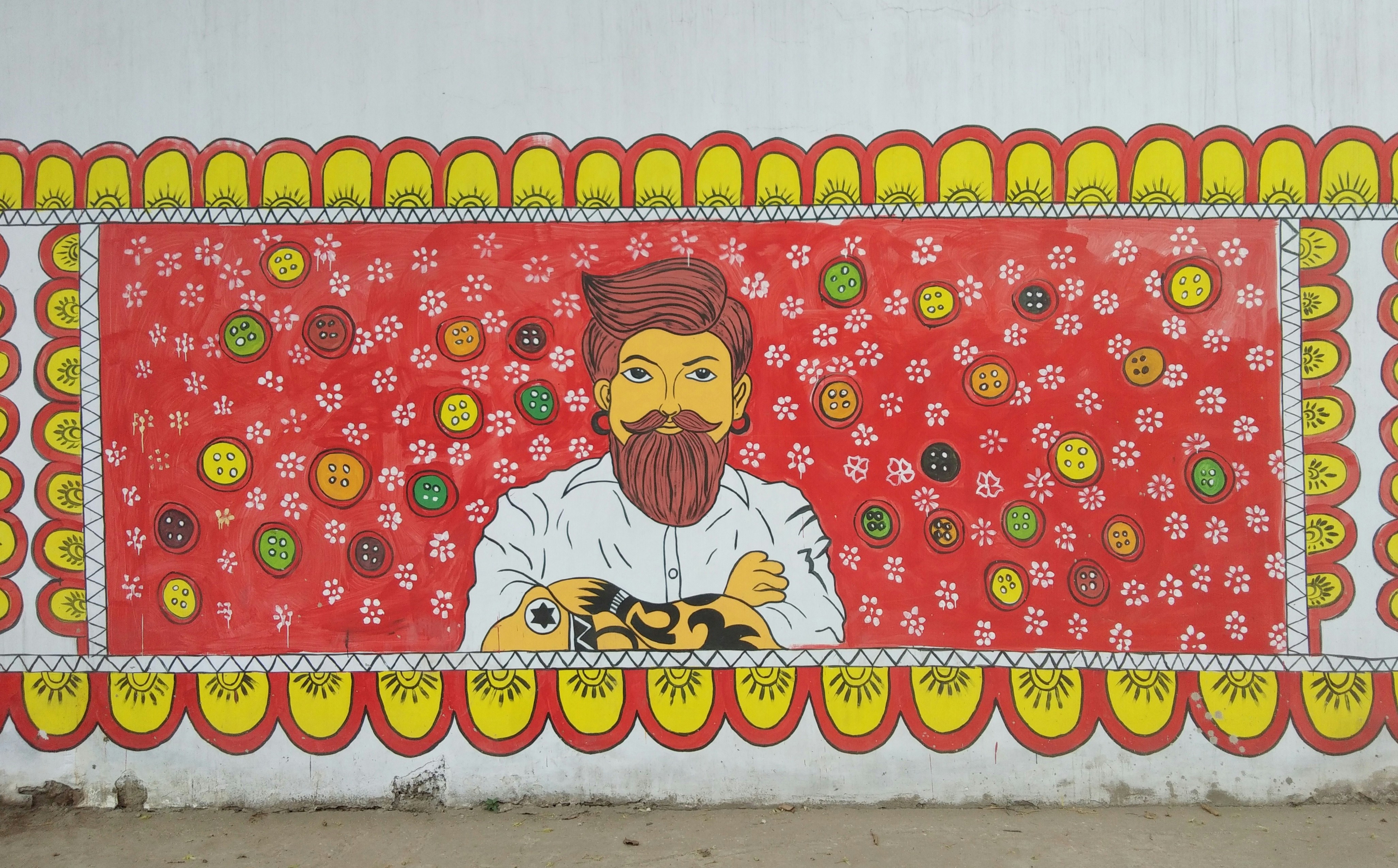 Wall mural painting of a bearded man in a white shirt, set against a red field dotted with flowers and button-like motifs, framed by a yellow scalloped border.