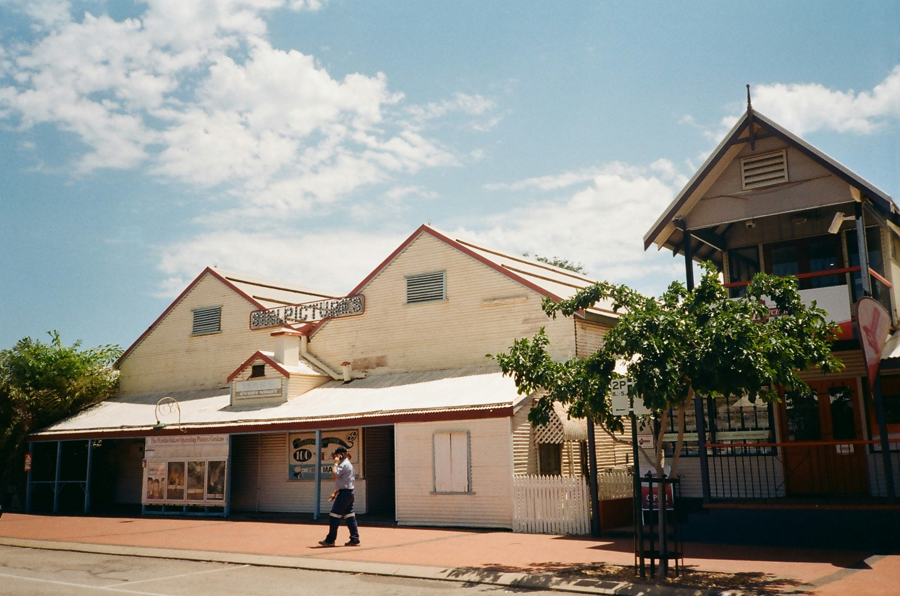 Historic building with a vintage signage, showcasing local culture and architecture. A passerby strolls along the sidewalk under a bright blue sky.
