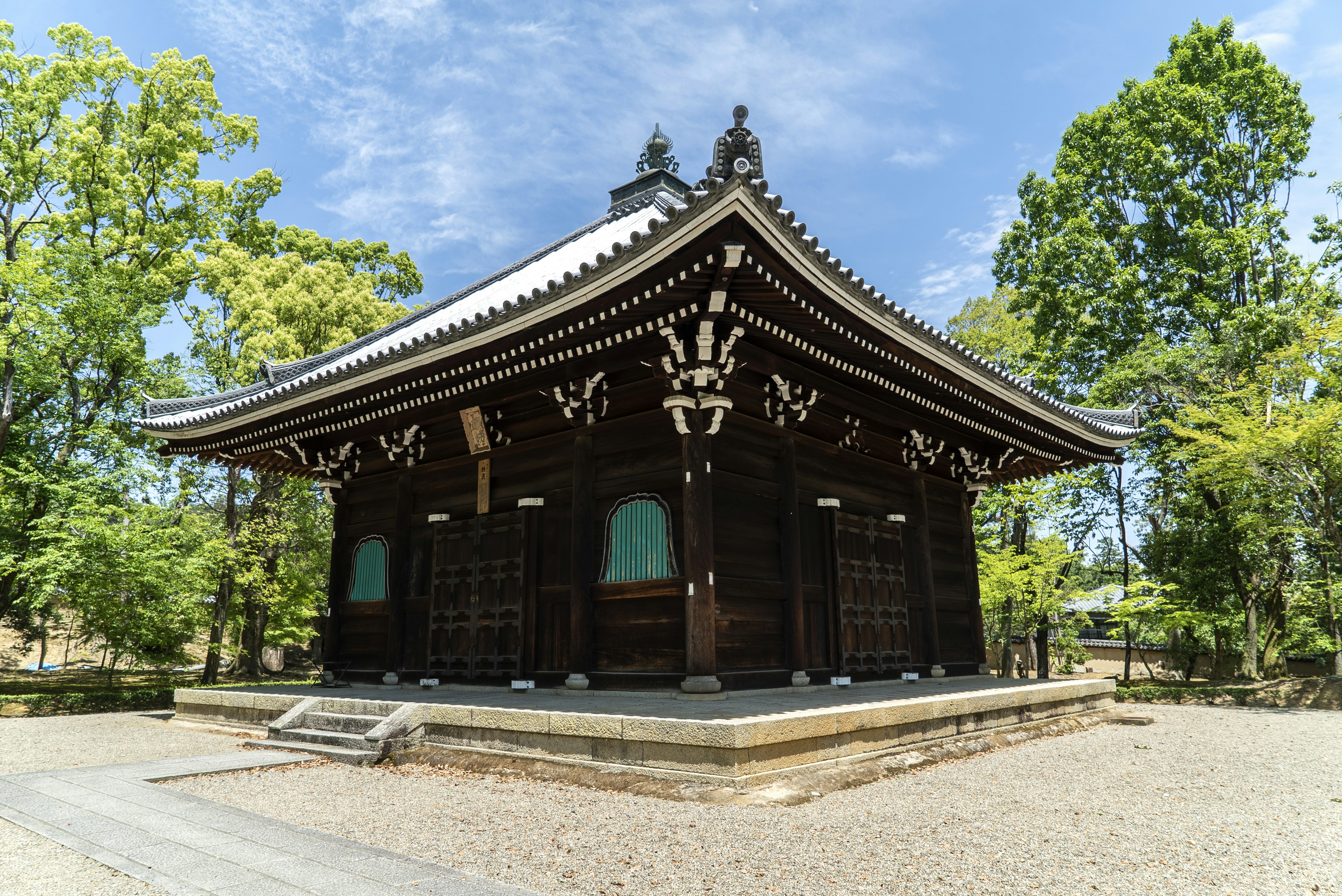 Traditional wooden temple surrounded by lush green trees under a clear blue sky.