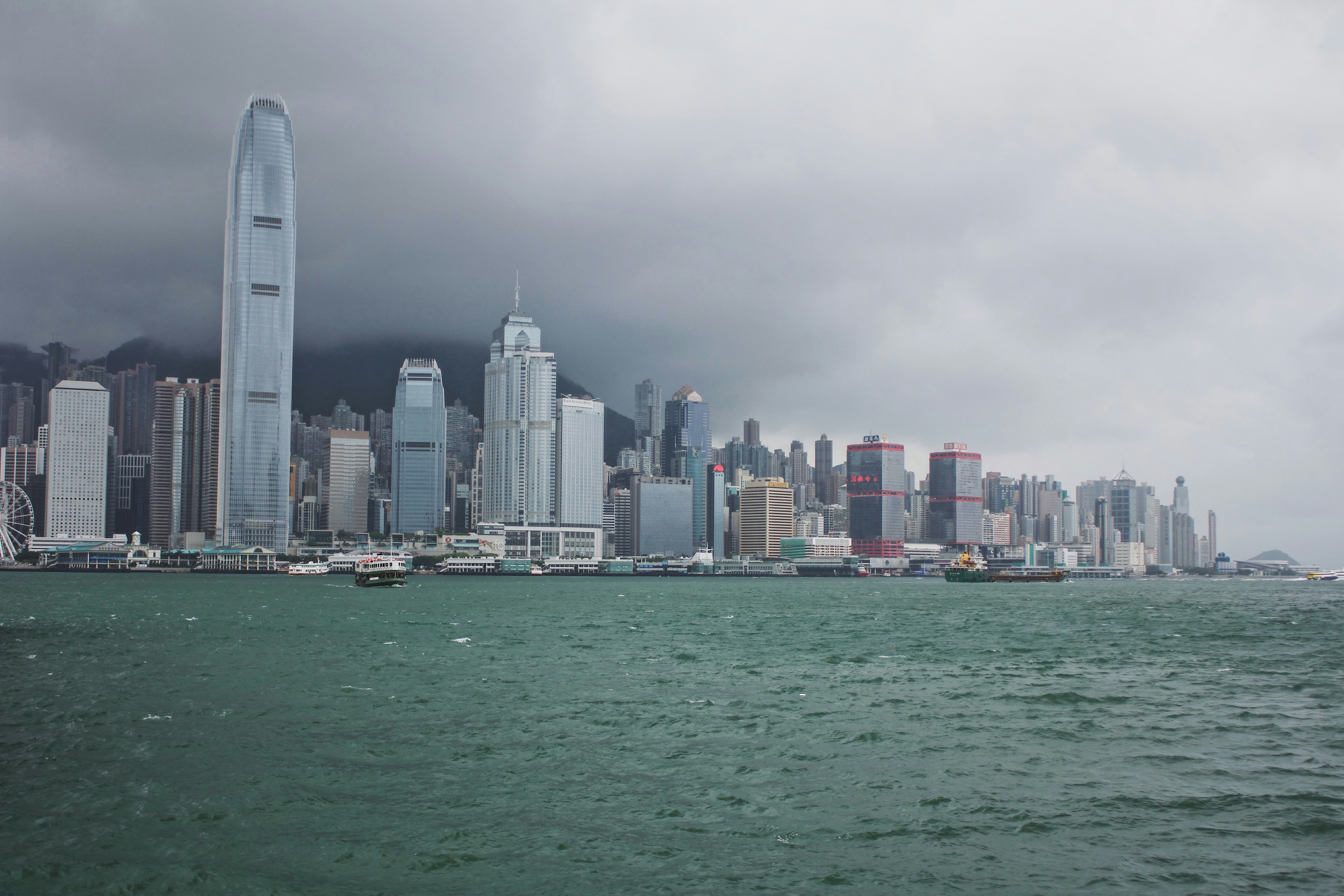 Modern skyline with towering skyscrapers against overcast skies and a choppy green sea.