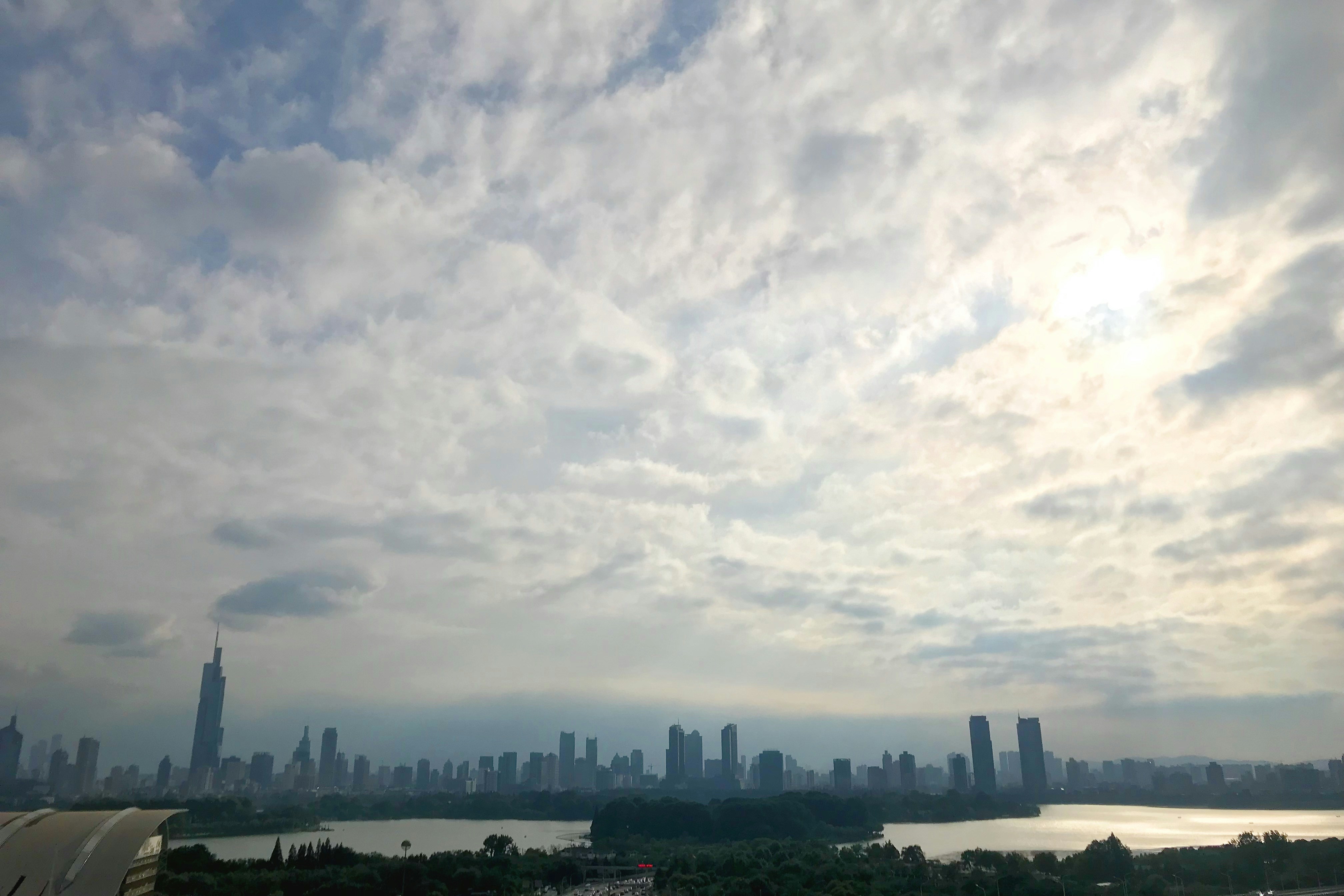 City skyline beneath a vast, cloud-filled sky with a body of water in the foreground.