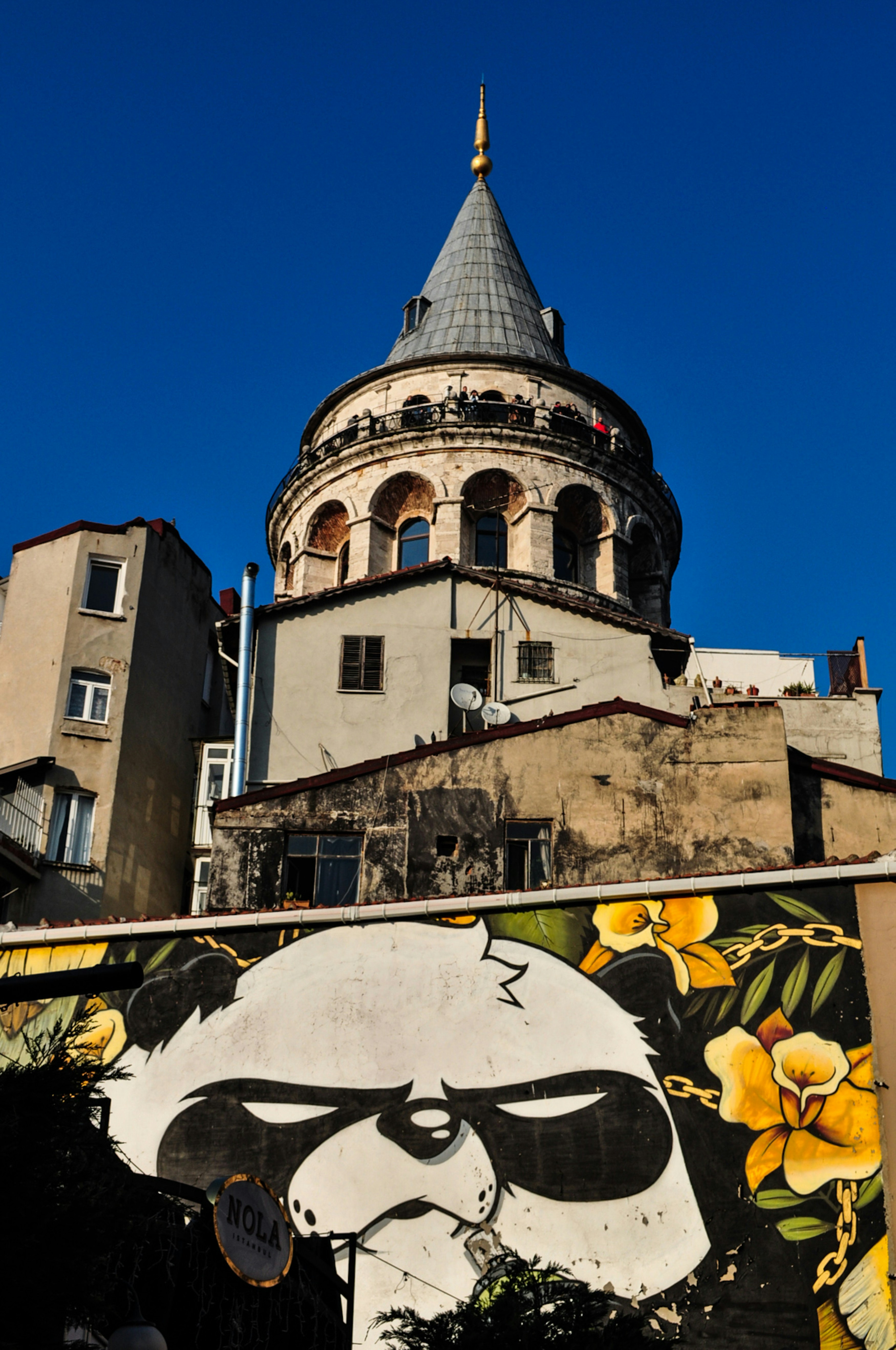 Towering stone structure with a pointed roof above a vibrant panda graffiti mural featuring yellow flowers.