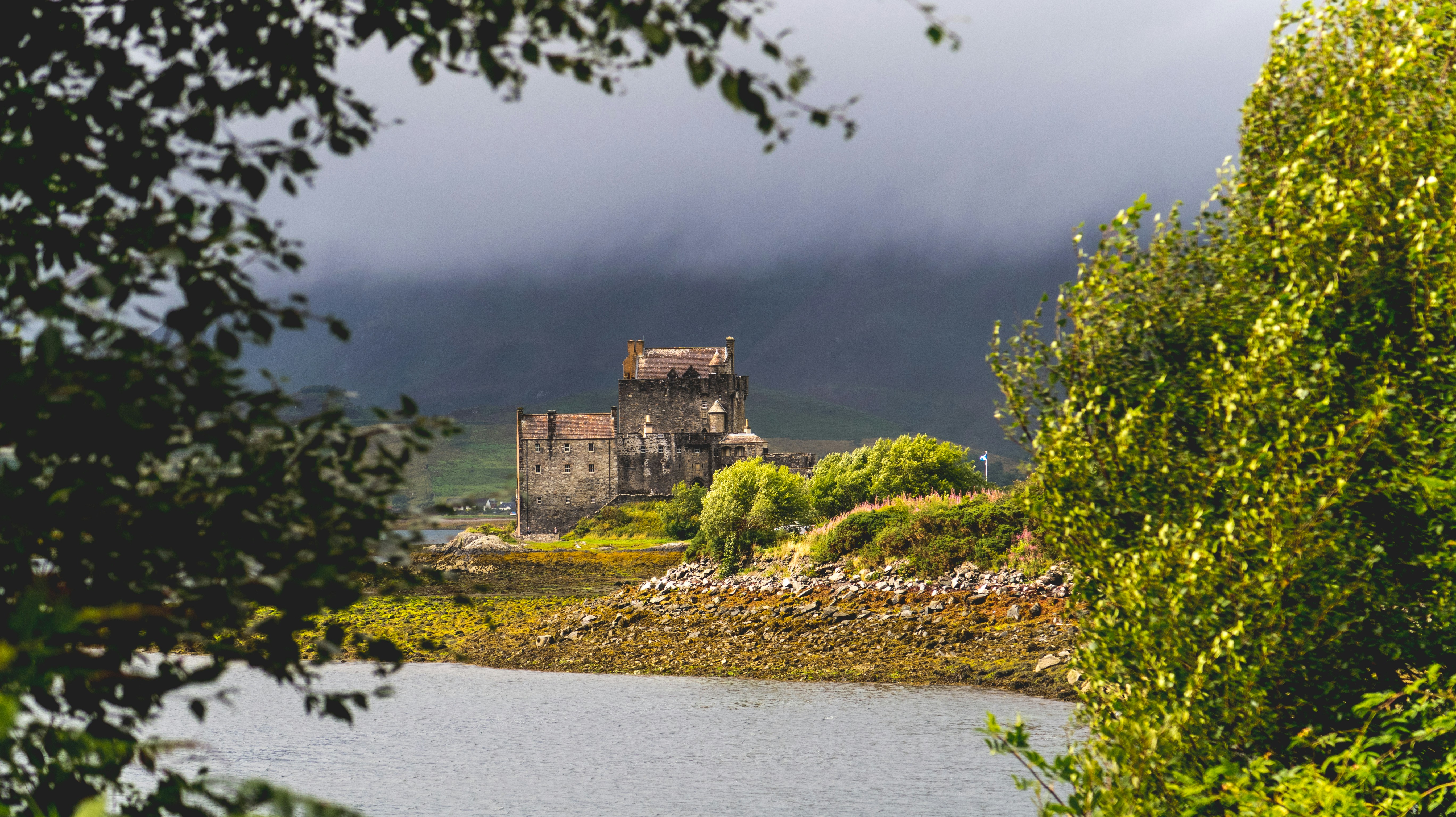 Ancient stone structure framed by lush greenery under a moody, overcast sky.