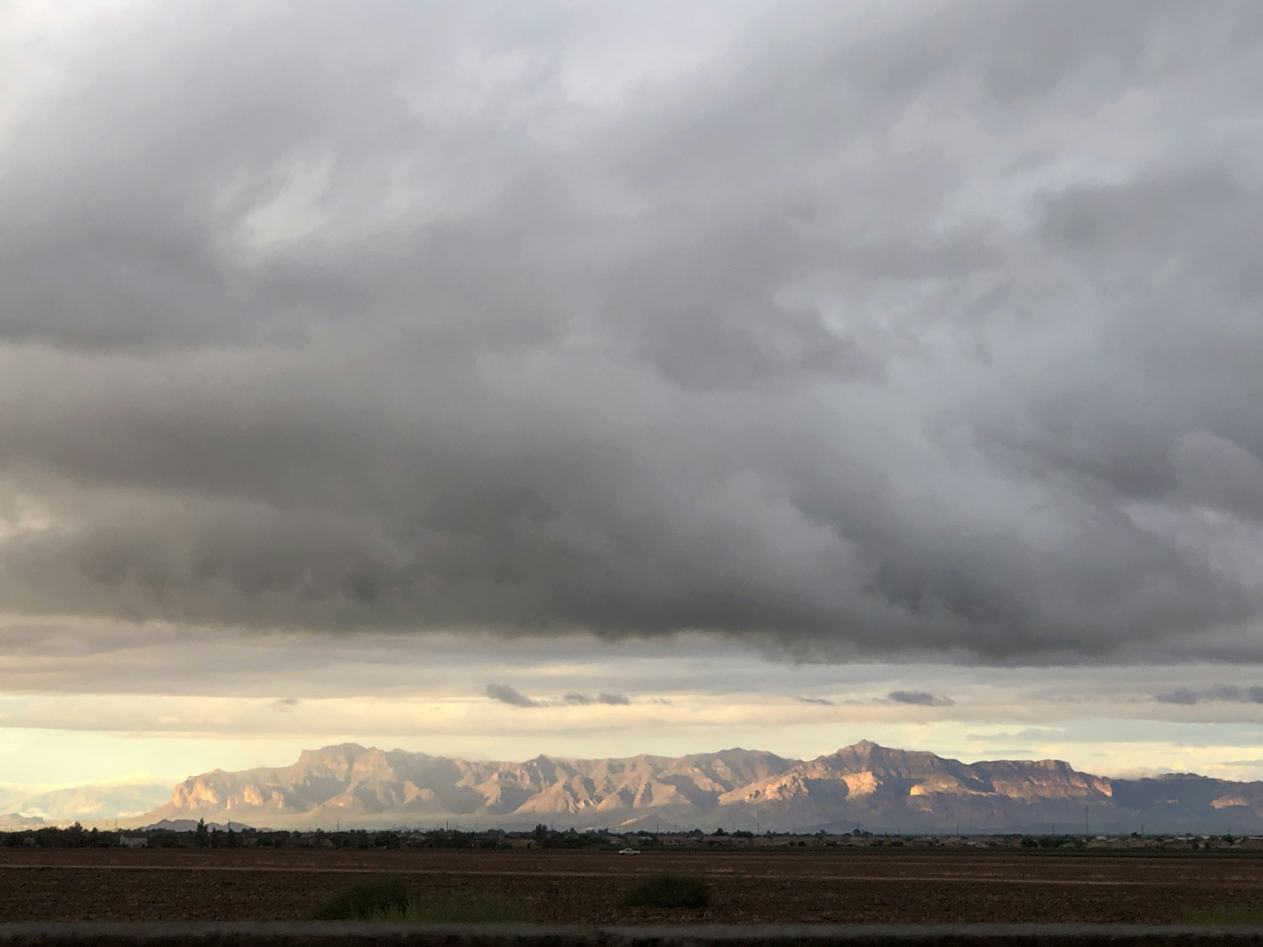 Cloud-laden sky stretches over a vast field, with sunlit mountains in the distance.