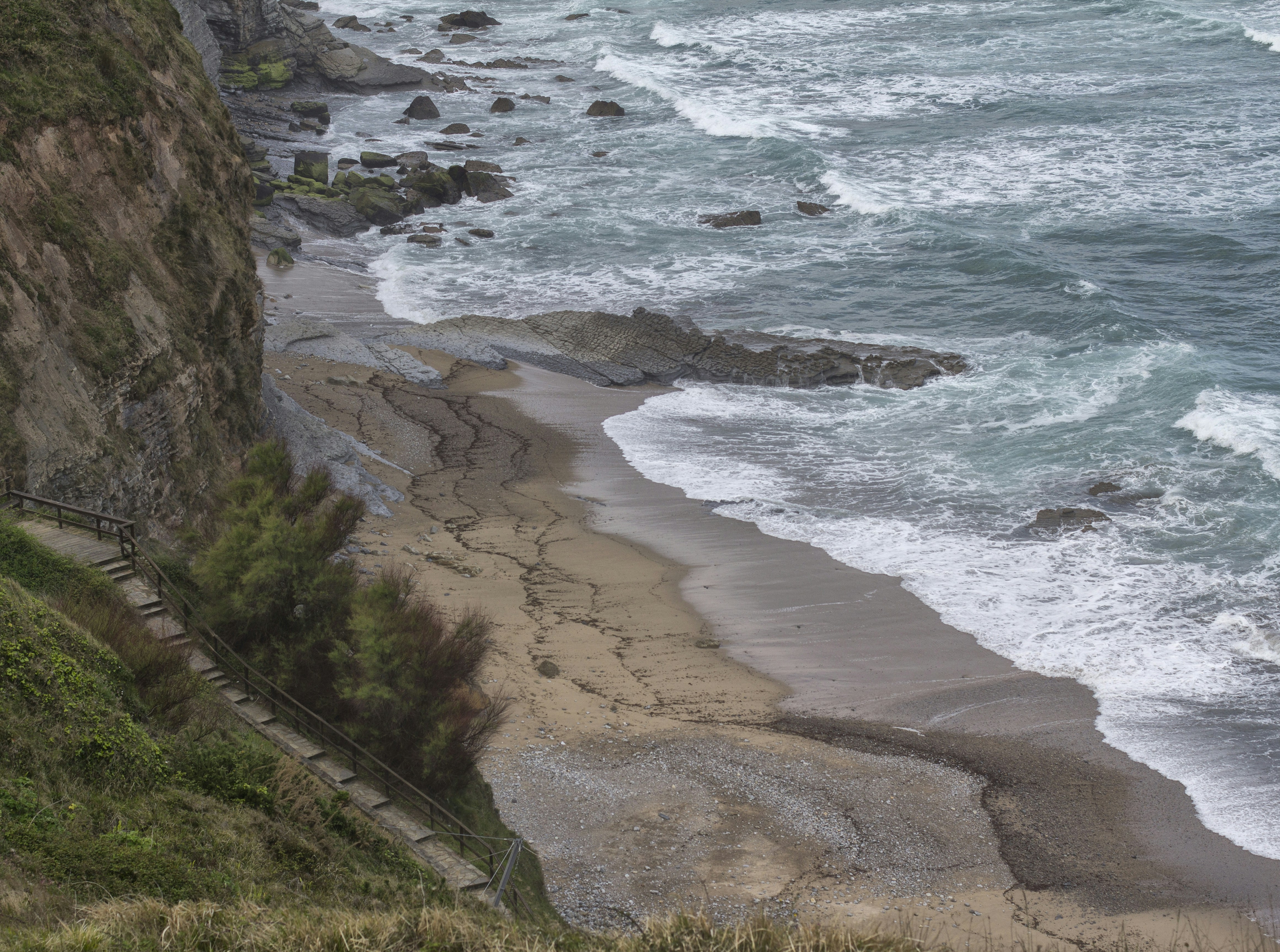Aerial view of a rocky coastline where waves gently lap against a narrow sandy beach.