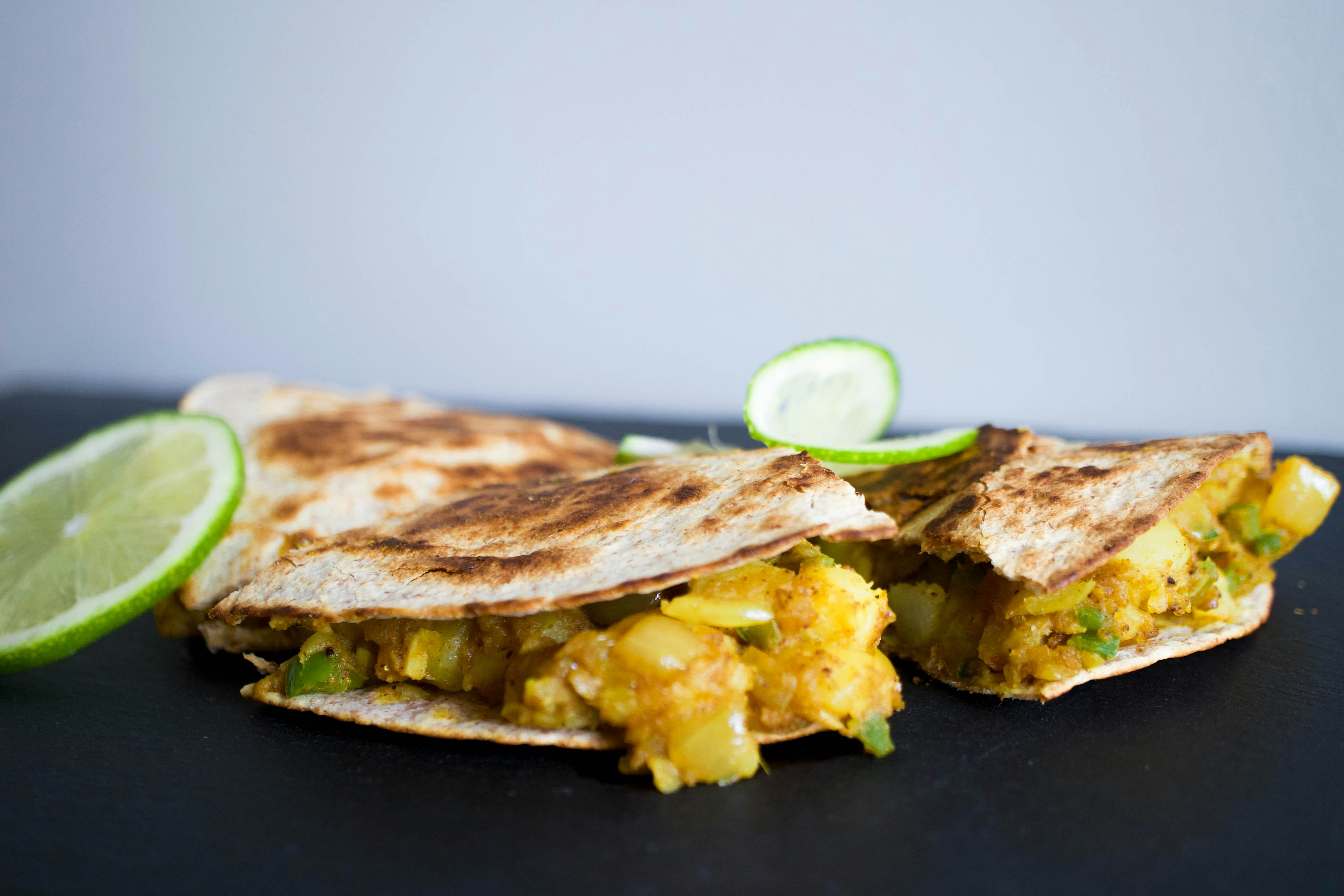 Two curry-filled quesadillas garnished with lime slices on a dark surface.