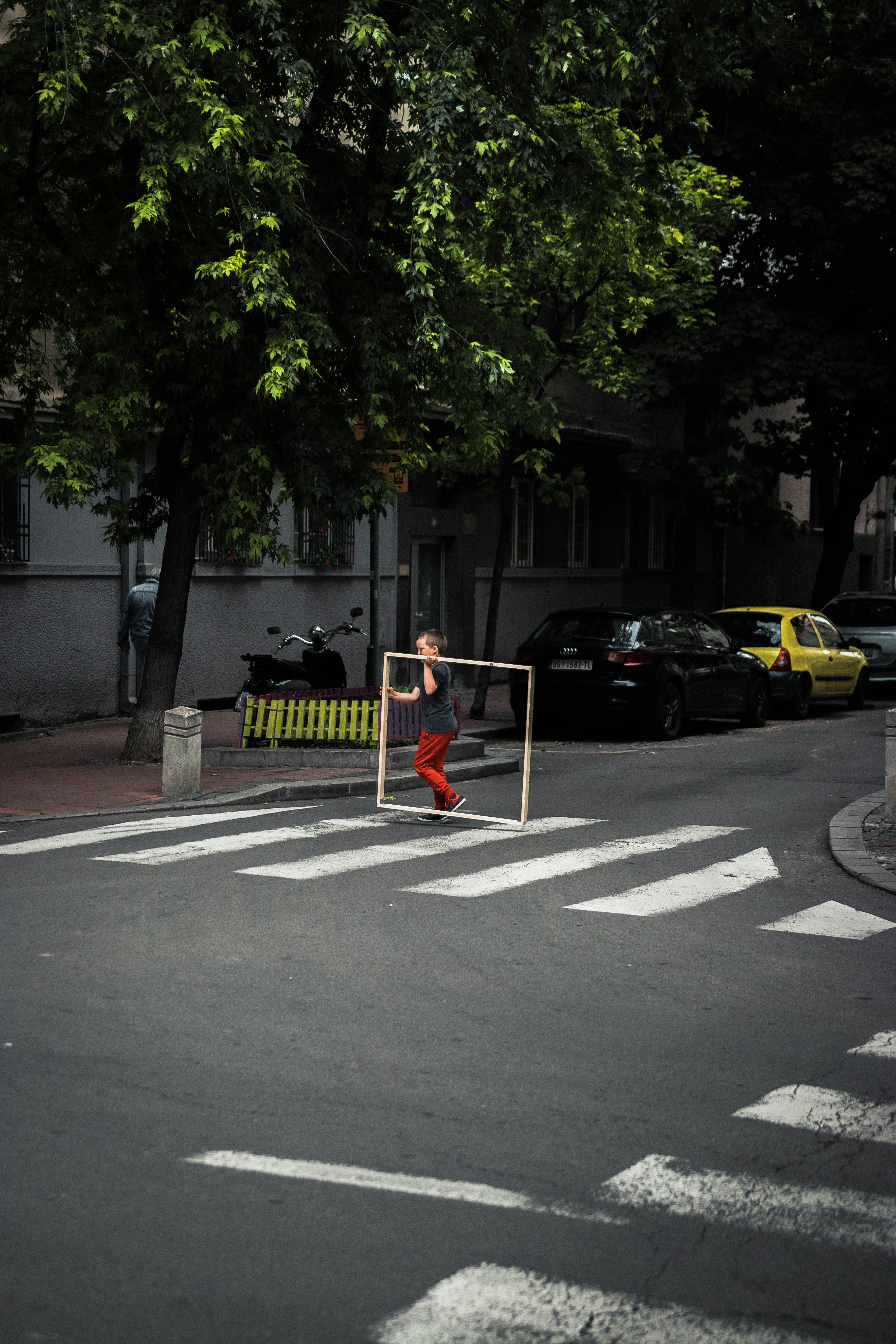 Frame on the Crosswalk: A lone figure in red traverses a wooden rectangle on a quiet city street