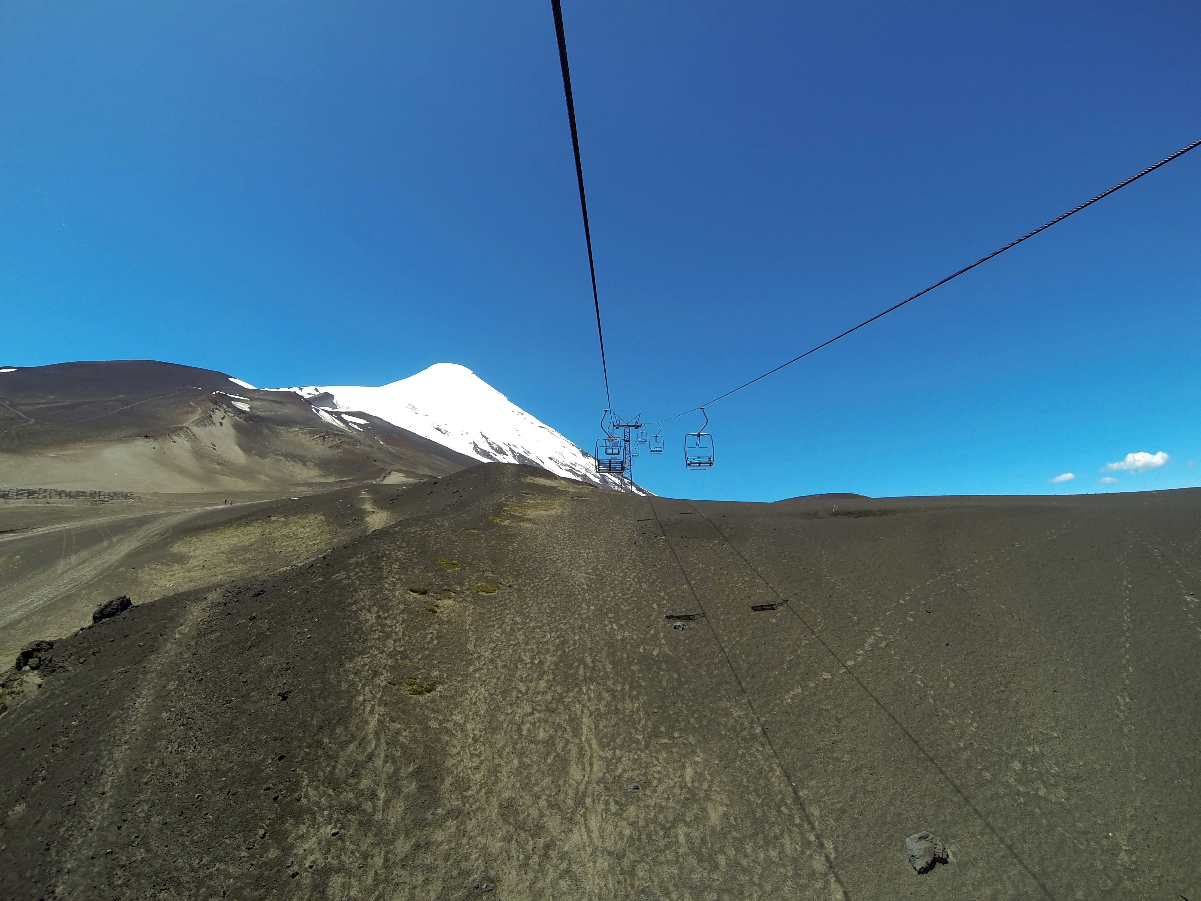 Snow-capped volcano peak with barren, rocky slopes under a bright blue sky.