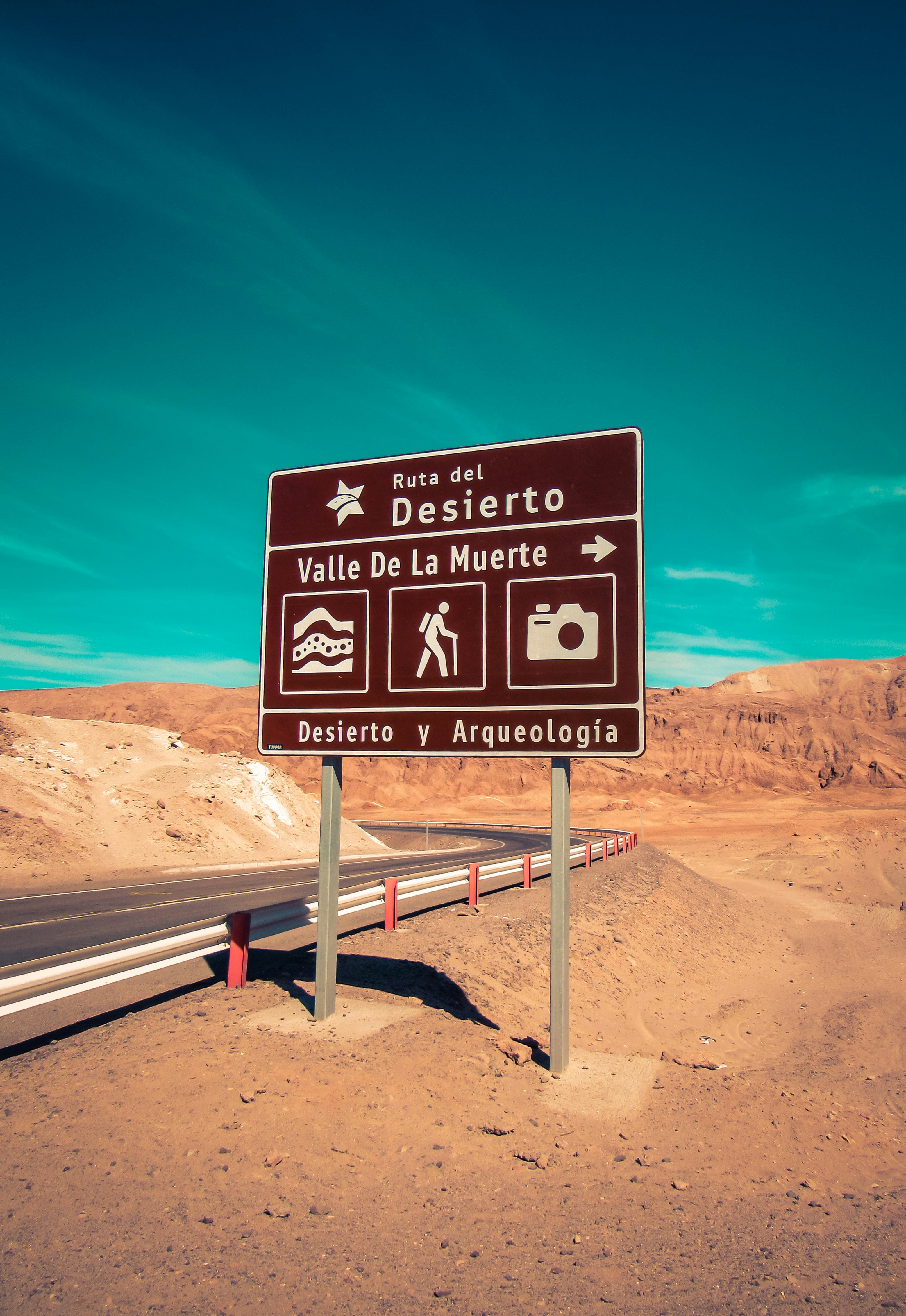 Brown road sign in a desert landscape with clear blue sky, directing towards Valle De La Muerte and archaeological sites.