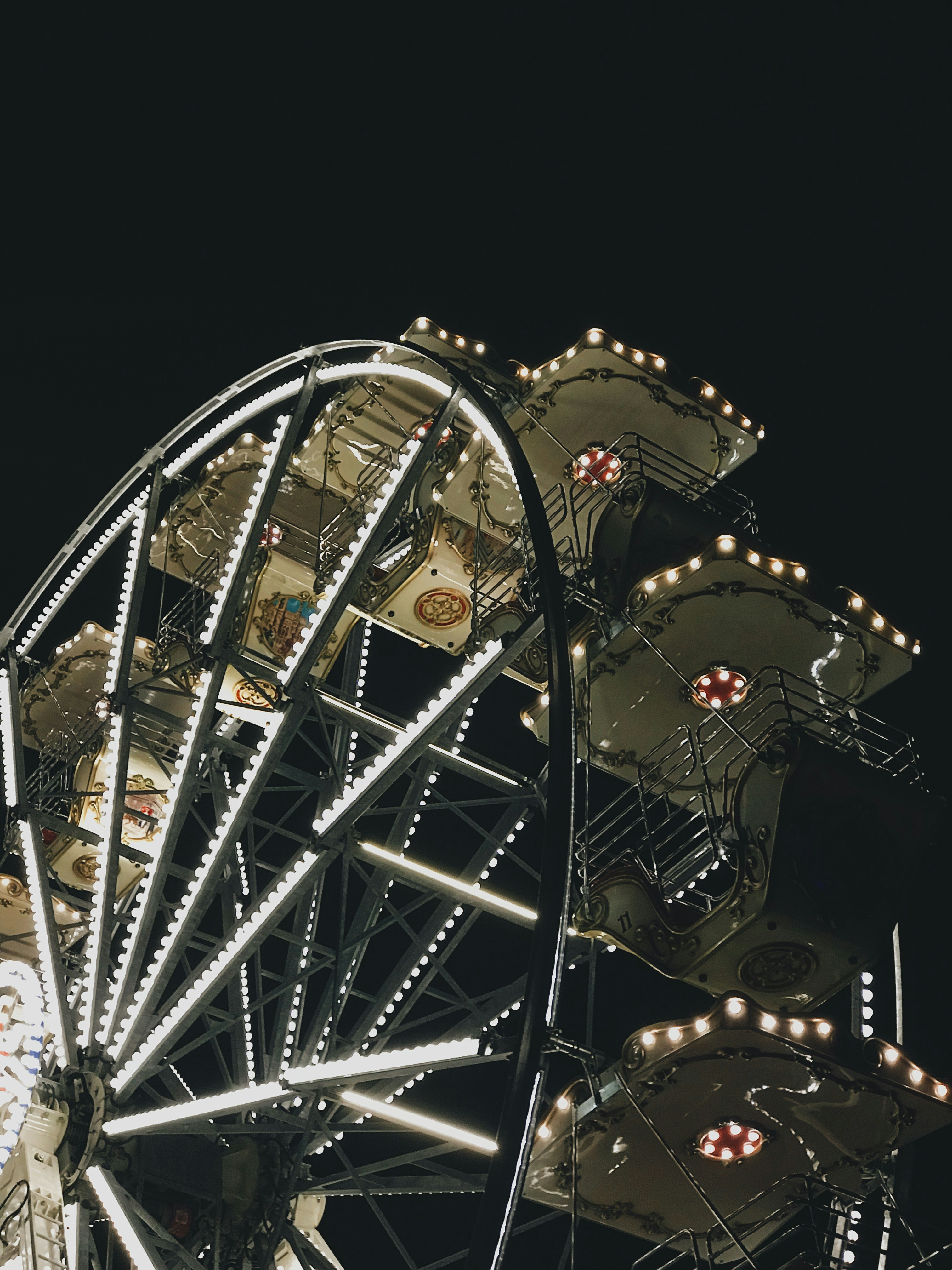 A Ferris wheel adorned with vibrant lights spins against a dark sky, showcasing its whimsical design and inviting atmosphere.