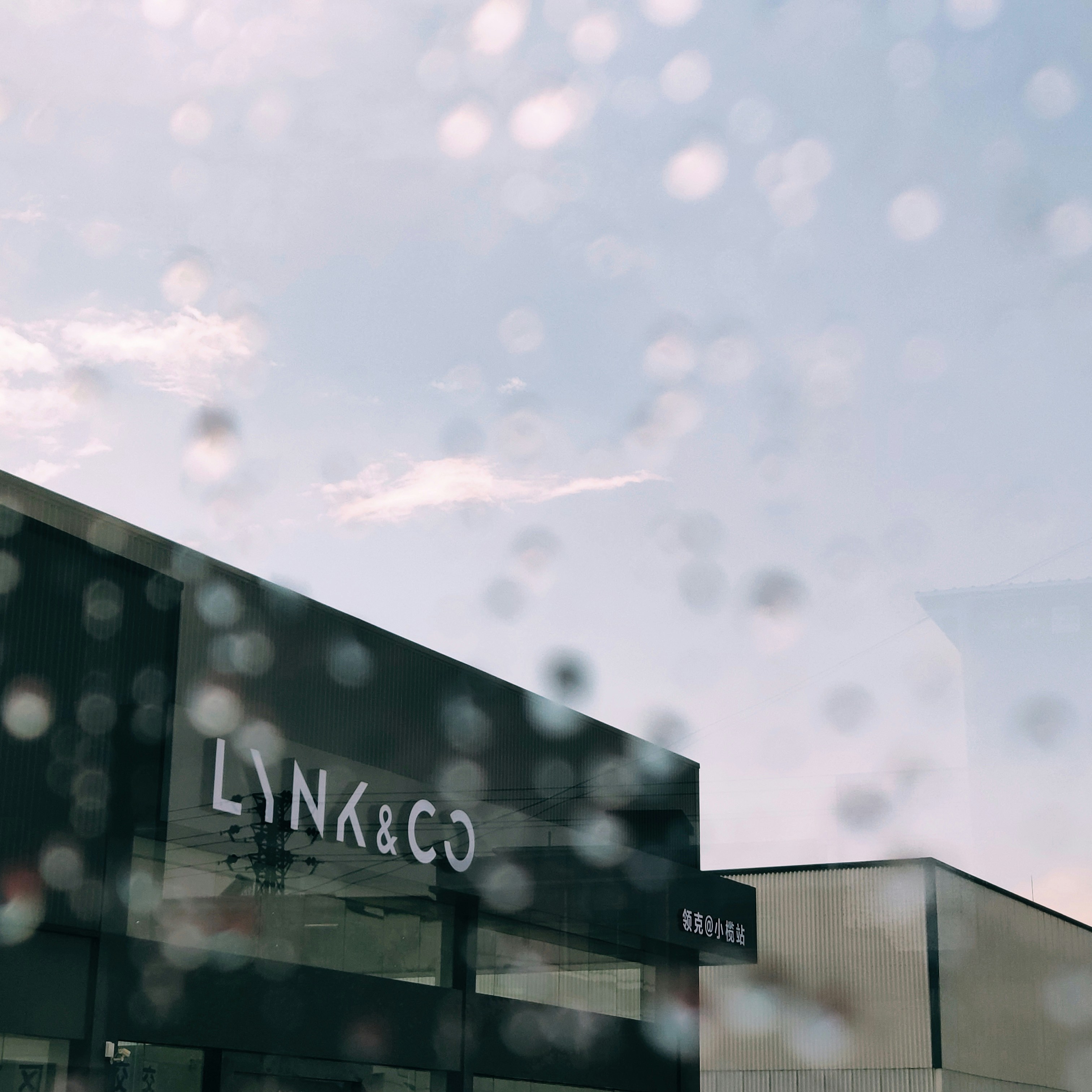 Raindrops on glass blur the view of a building under a clear sky.