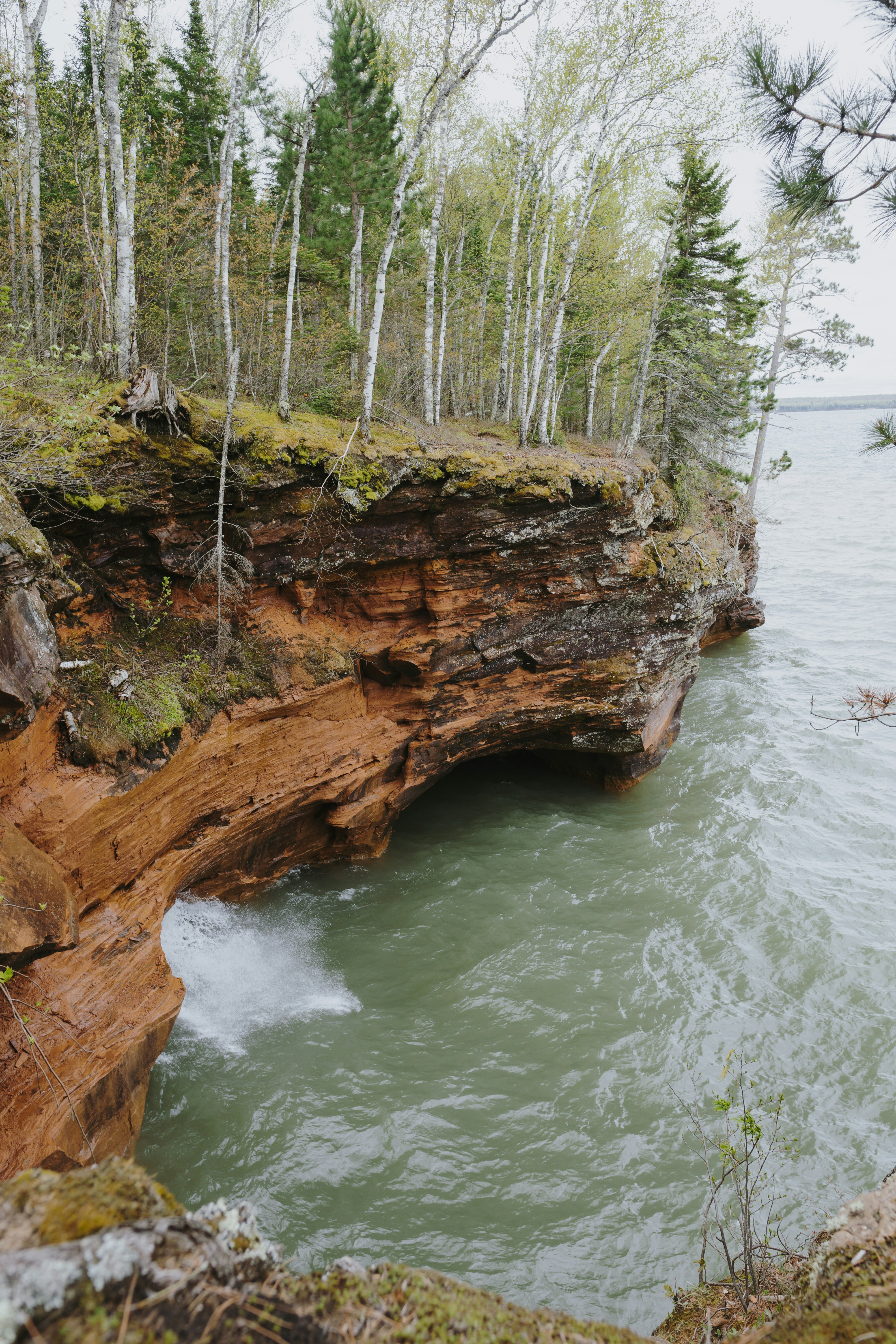 A rocky cliff with a body of water in the foreground photo – Free ...