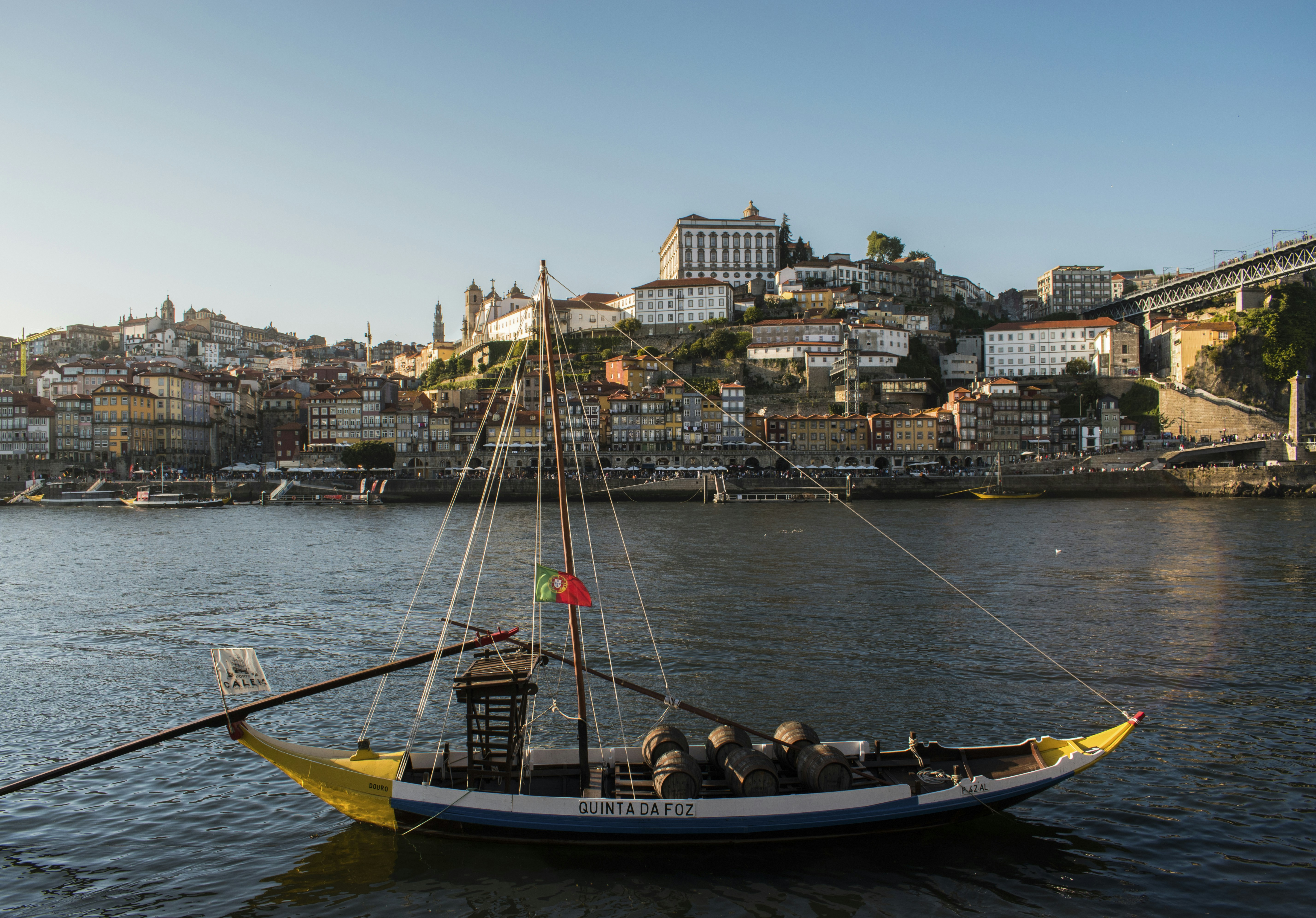 Traditional boat anchored on the Douro River with the historic cityscape of Porto in the background under a clear blue sky.