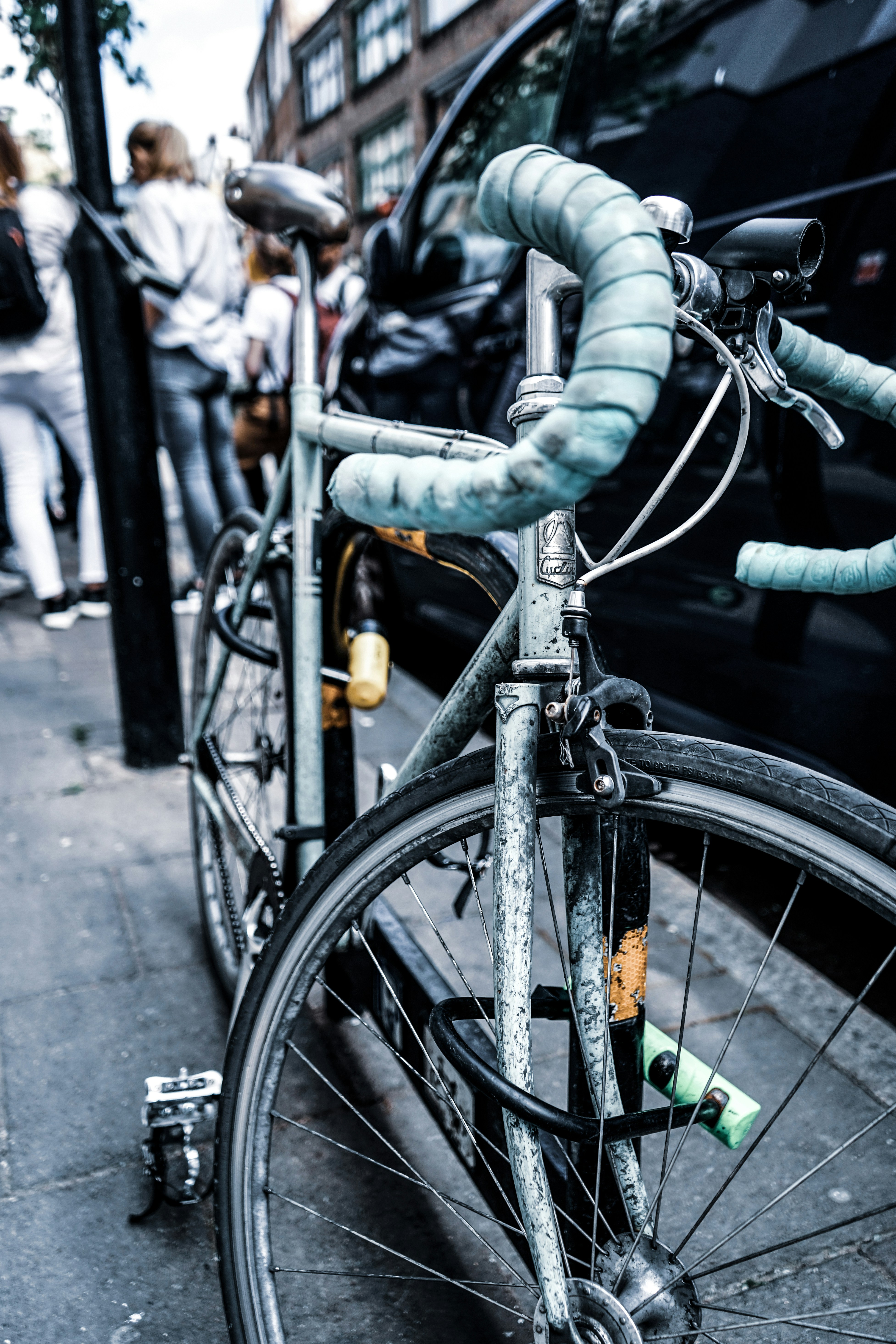 Teal-wrapped handlebars anchor a weathered bicycle in a busy urban frame