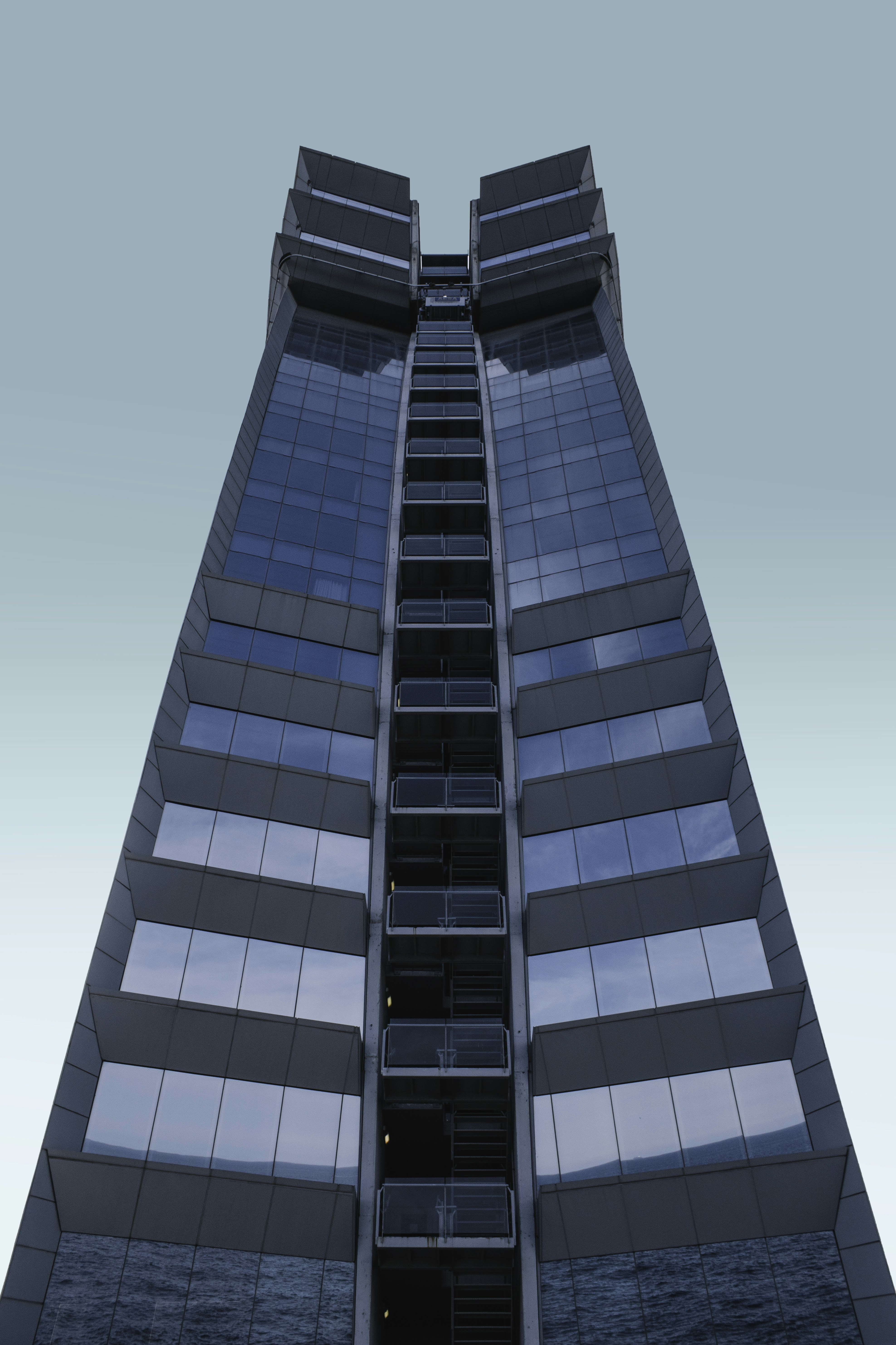Sleek, glass-clad skyscraper rising towards the sky, showcasing a unique symmetrical design with balconies and reflective surfaces.