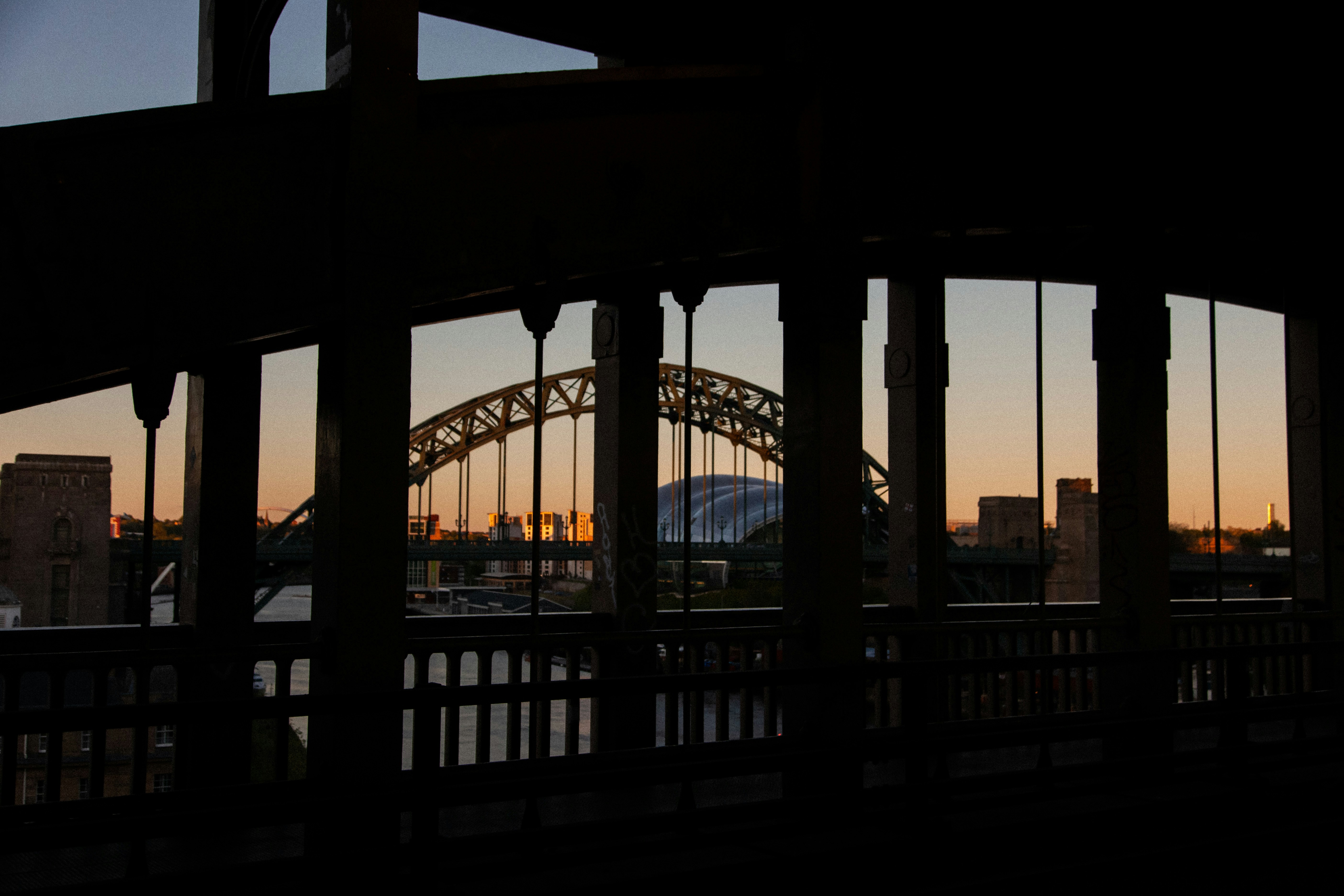 Silhouetted bridge arches frame a cityscape against a vibrant sunset sky.