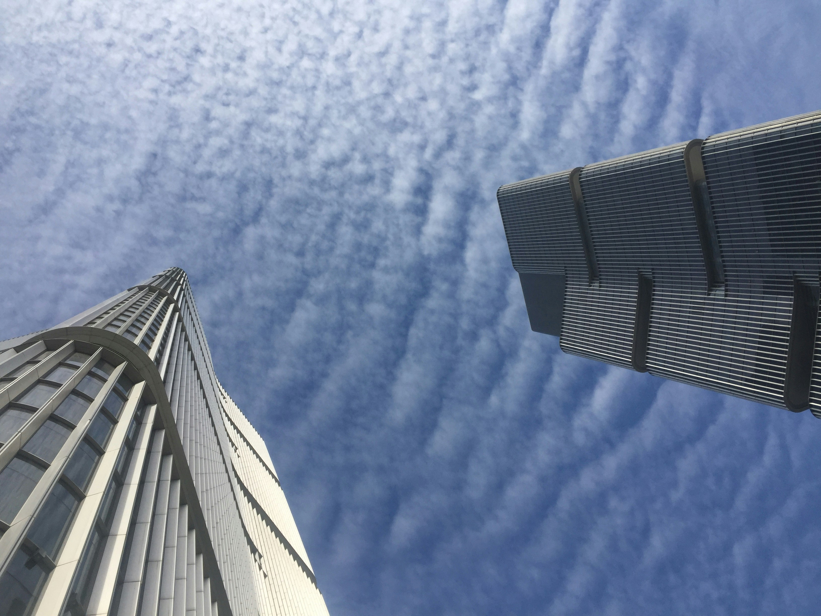 Two towering skyscrapers reaching toward a textured sky, showcasing modern architectural design against a backdrop of wispy clouds.