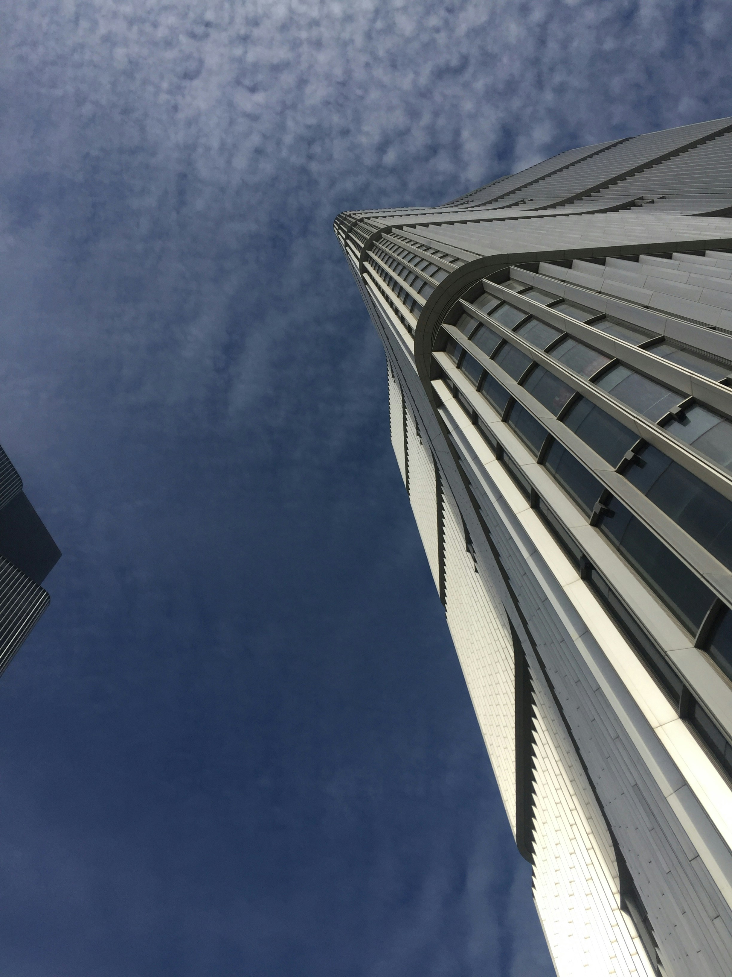 A modern skyscraper stretches upward against a backdrop of textured clouds, showcasing its sleek lines and reflective surfaces.