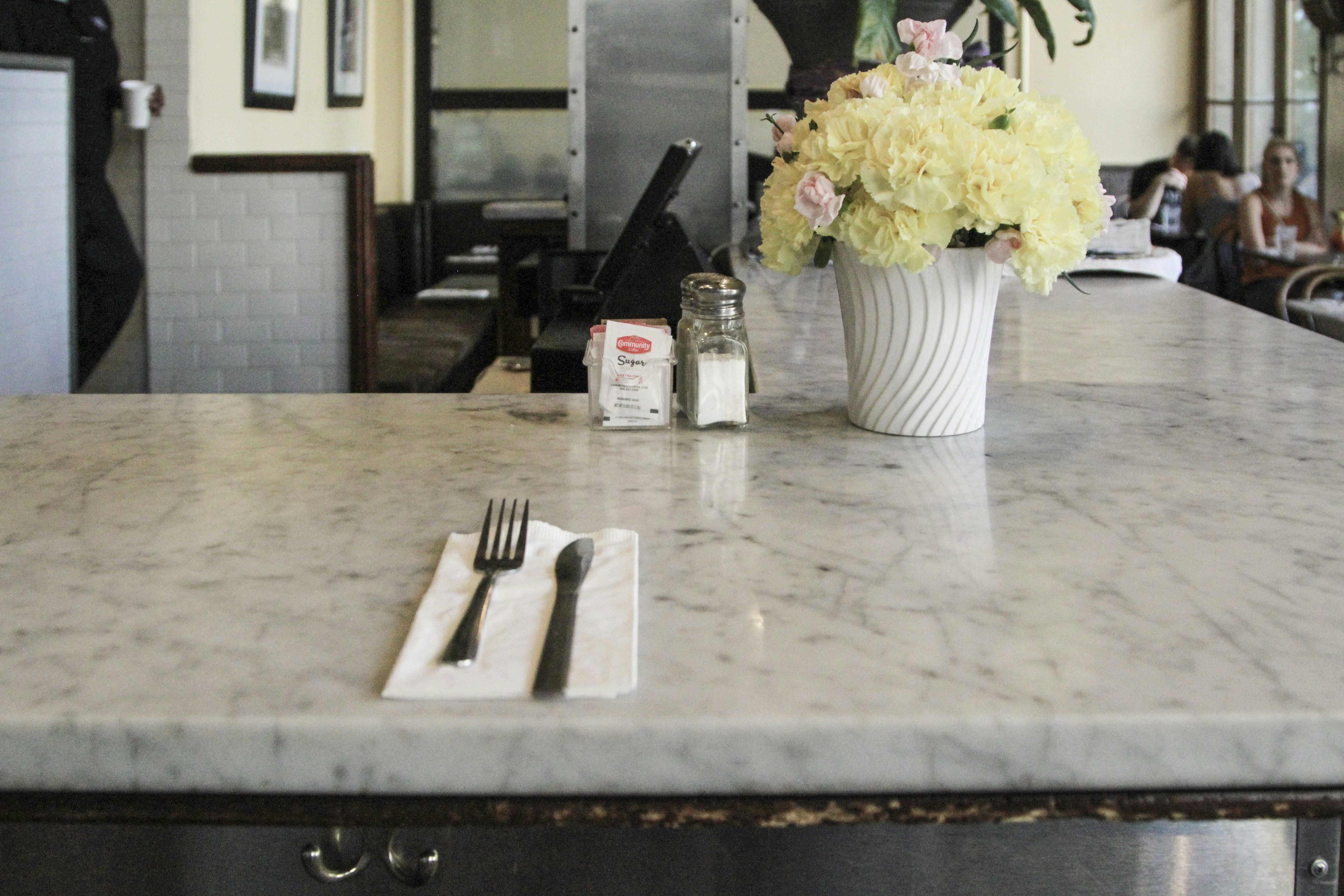 Polished Quiet at the Counter: Cutlery and Florals in Soft Café Light
