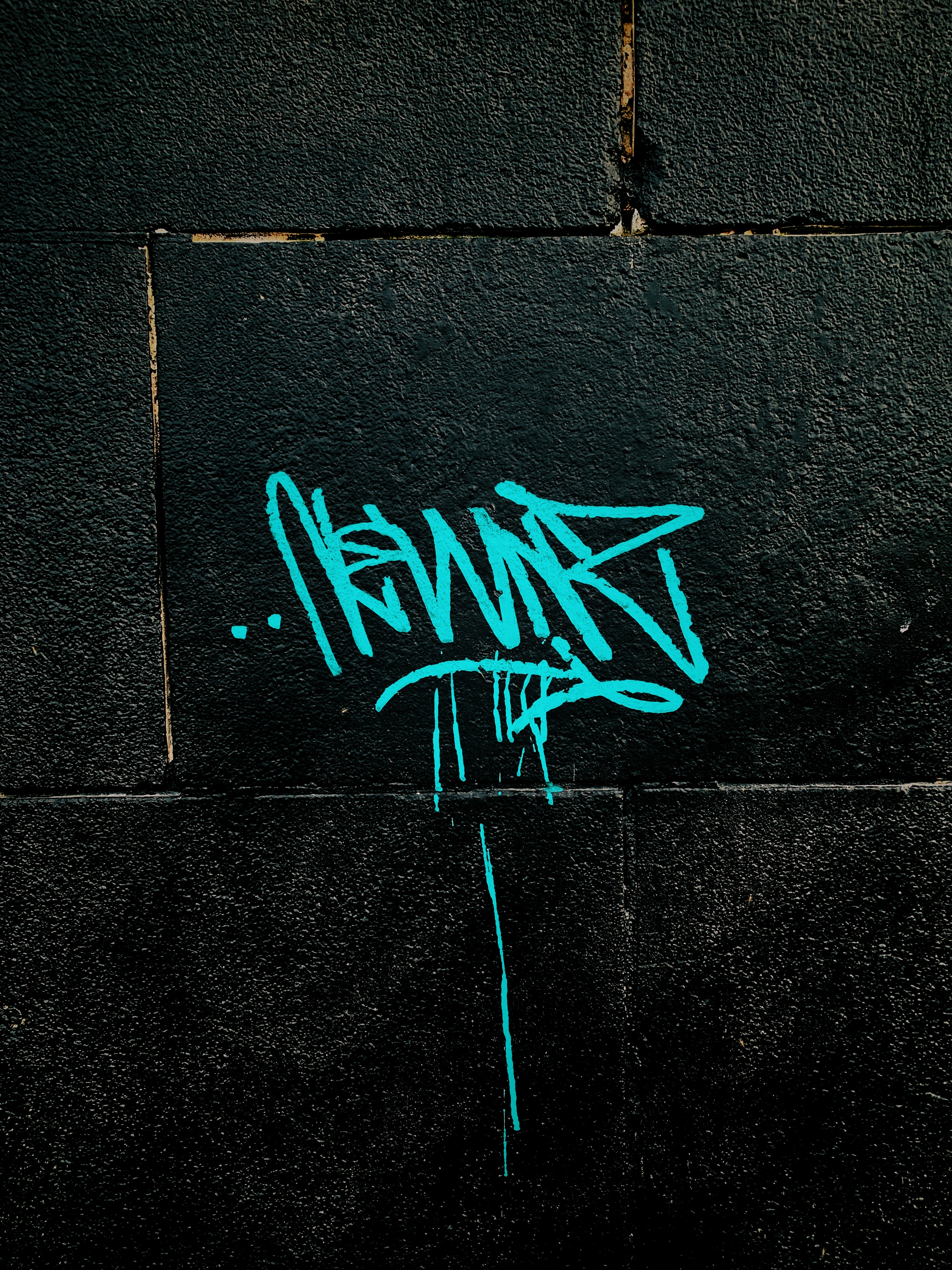 Turquoise graffiti art splashed across a textured black wall, showcasing vibrant street culture.