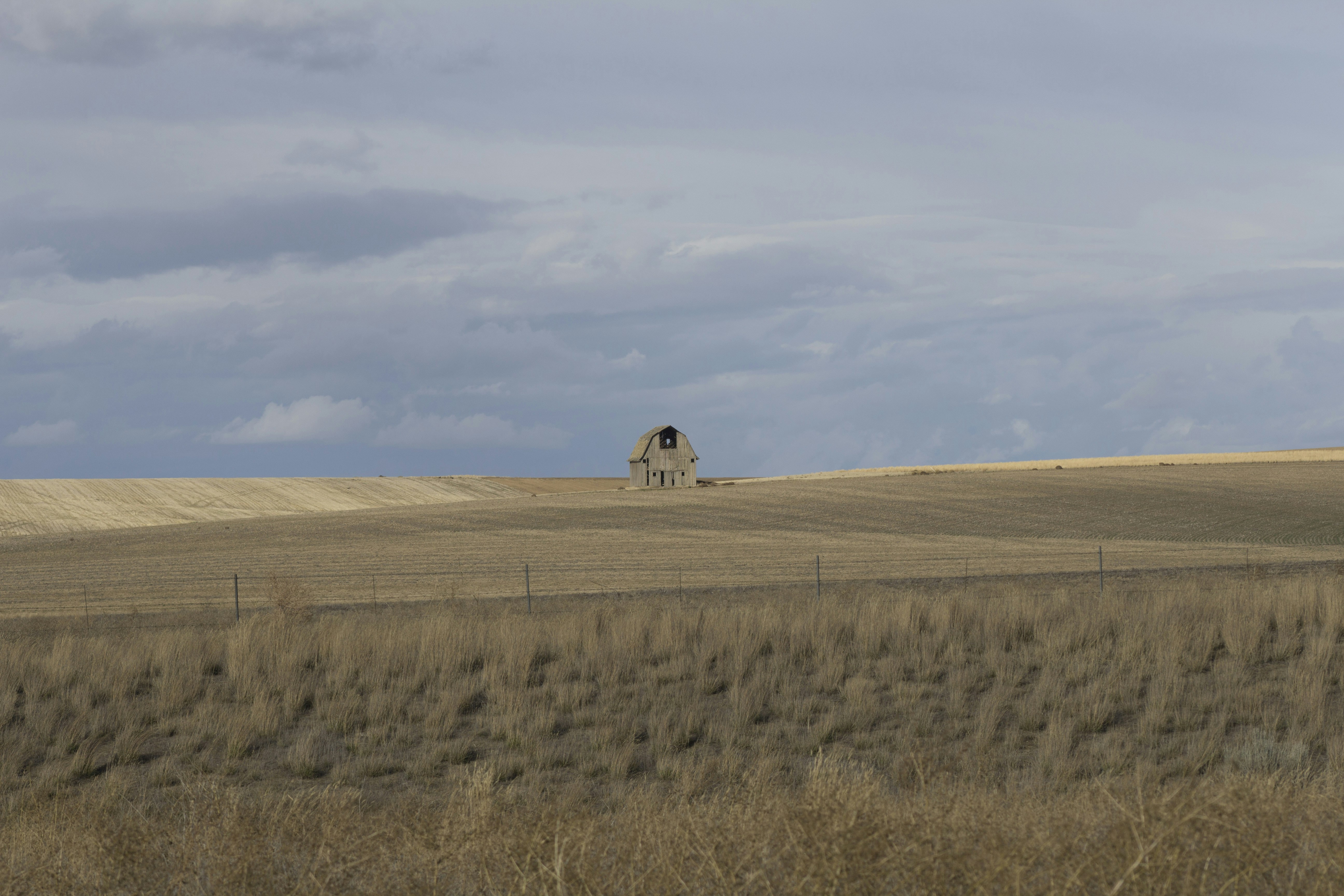 Weathered barn standing solitary against a vast, open landscape under a cloudy sky.