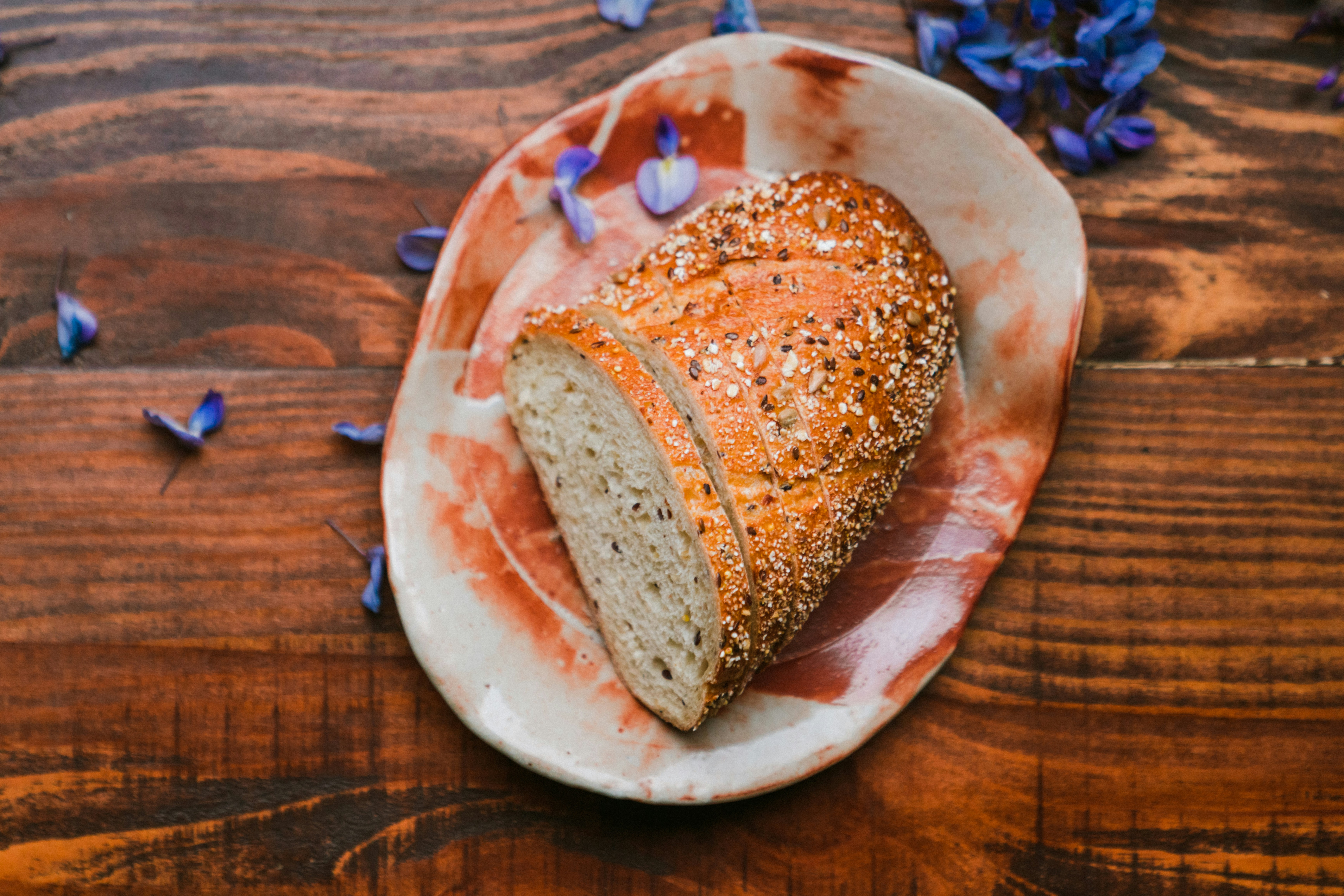 Freshly baked bread slice resting on a handcrafted plate, surrounded by delicate blue petals.