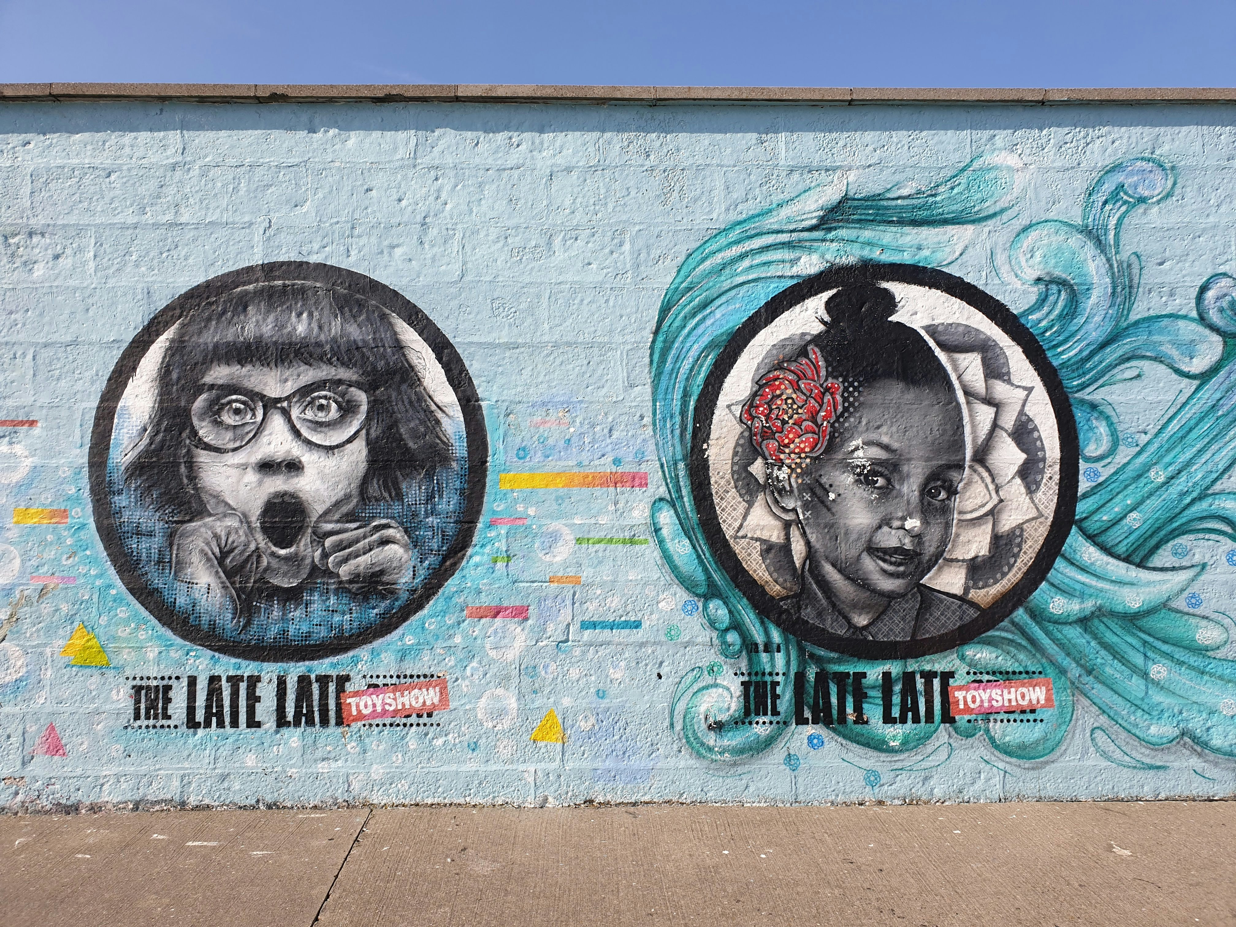 Vibrant mural featuring two expressive portraits, one of a girl with glasses and another of a girl with a flower in her hair, set against a textured blue background.